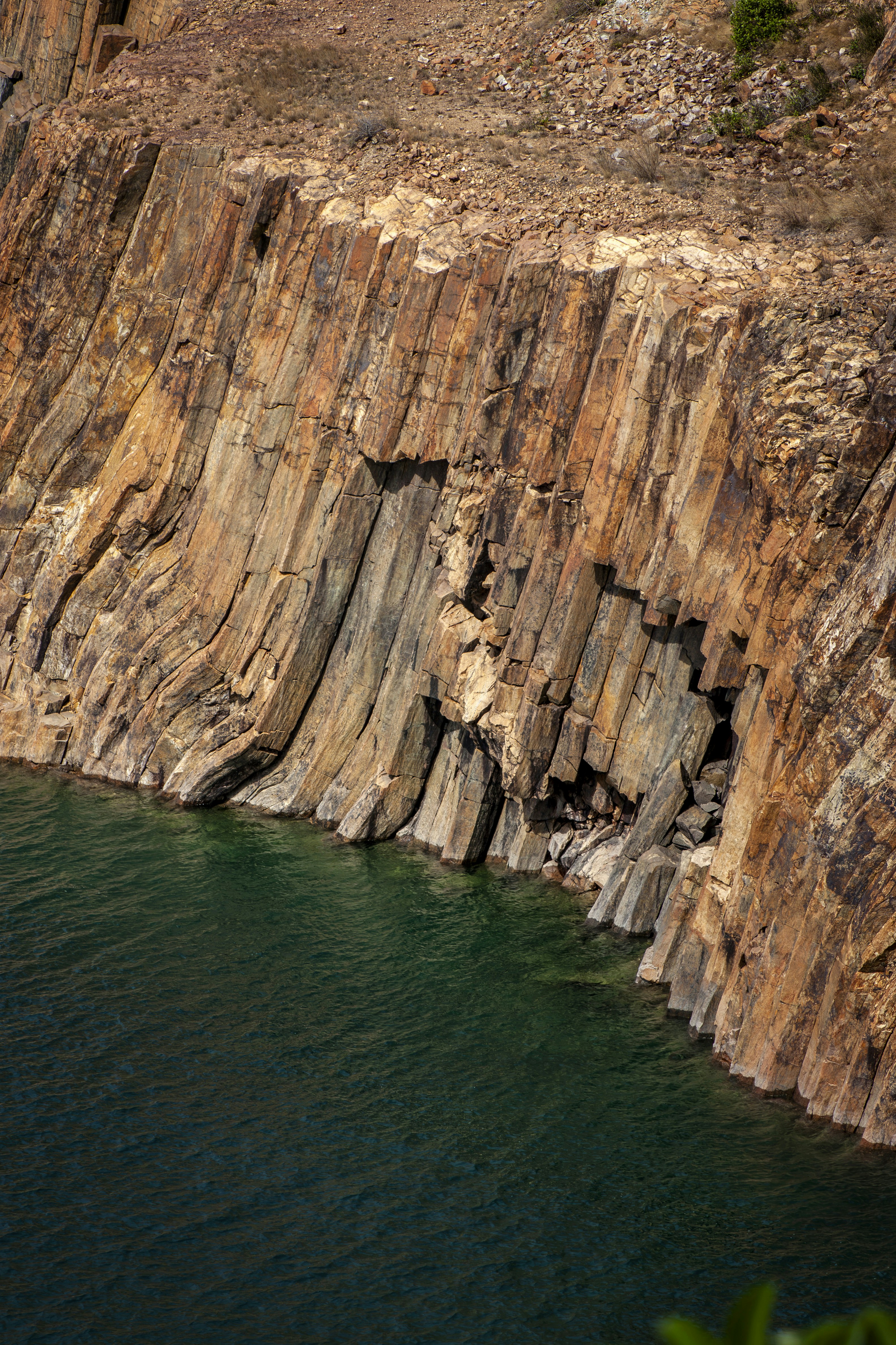 Intricate rock formations meet the tranquil waters, showcasing natural erosion patterns along a cliffside. The scene highlights the interplay between land and water.