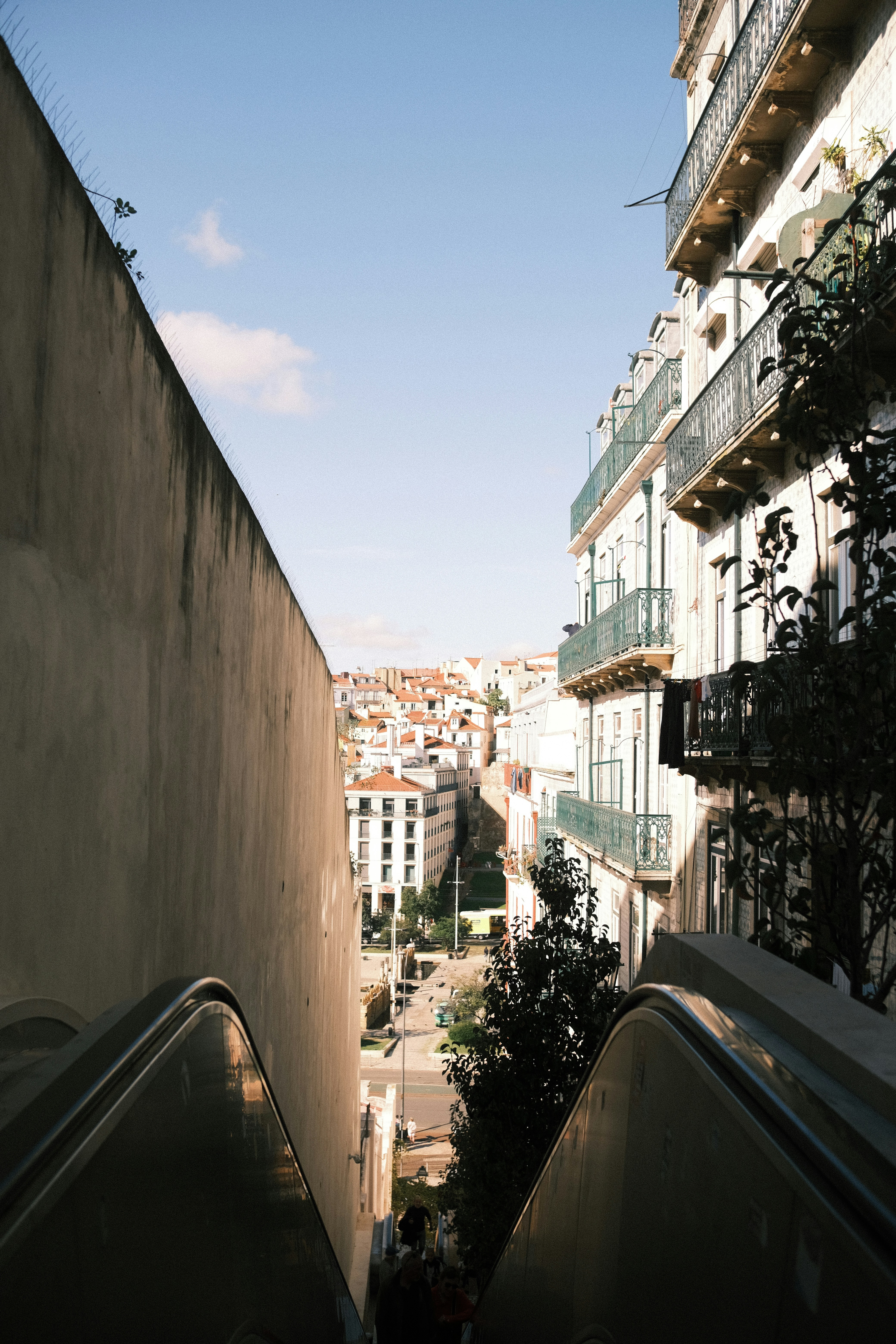 Escalators leading down towards a vibrant cityscape, framed by architectural details of Lisbon's buildings. The scene captures the essence of urban exploration.