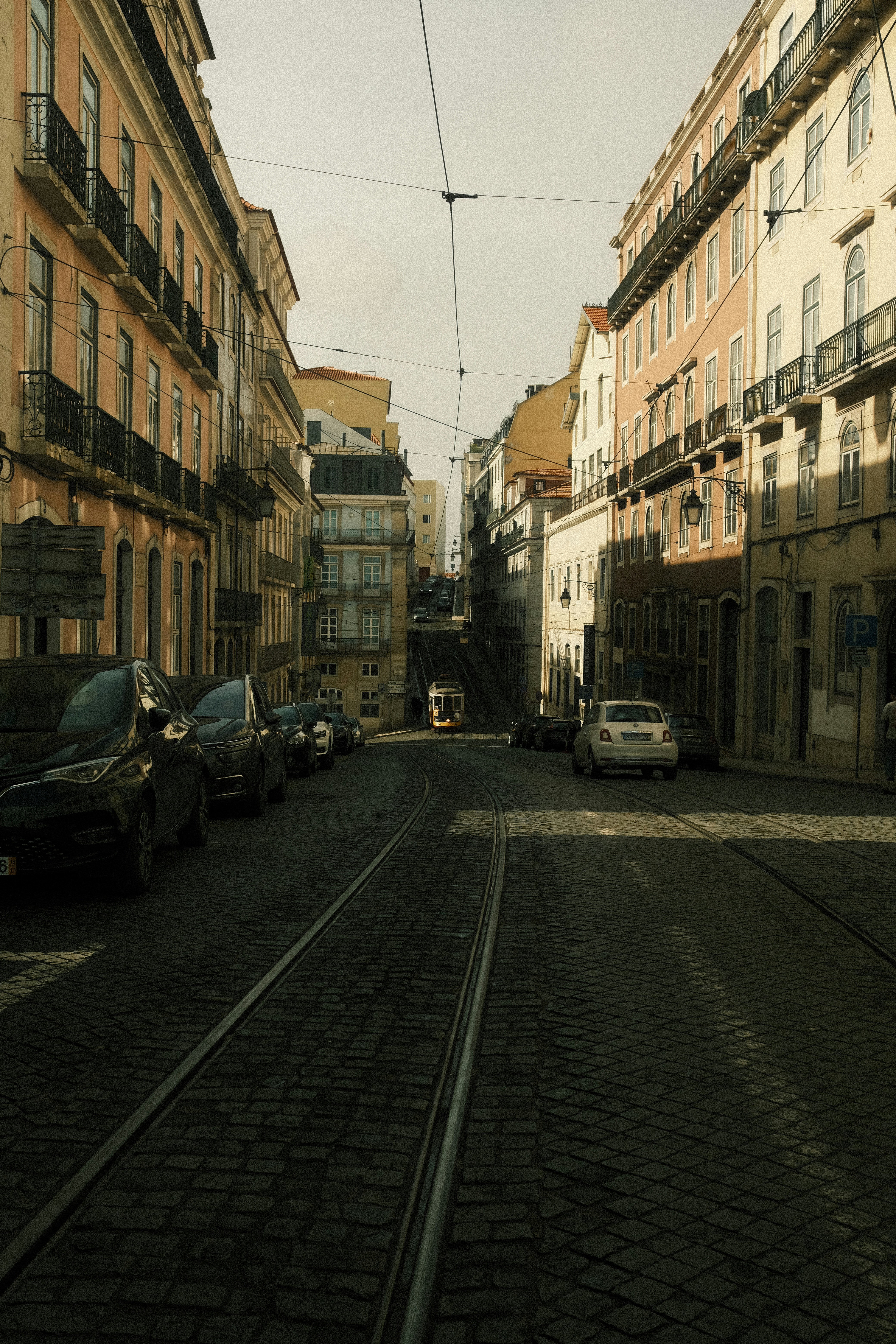 A picturesque European street glowing in soft sunlight, lined with colorful buildings and wrought-iron balconies. Ideal for travel, city life, or architectural visuals. | Trams on a cobblestone street in a european city.