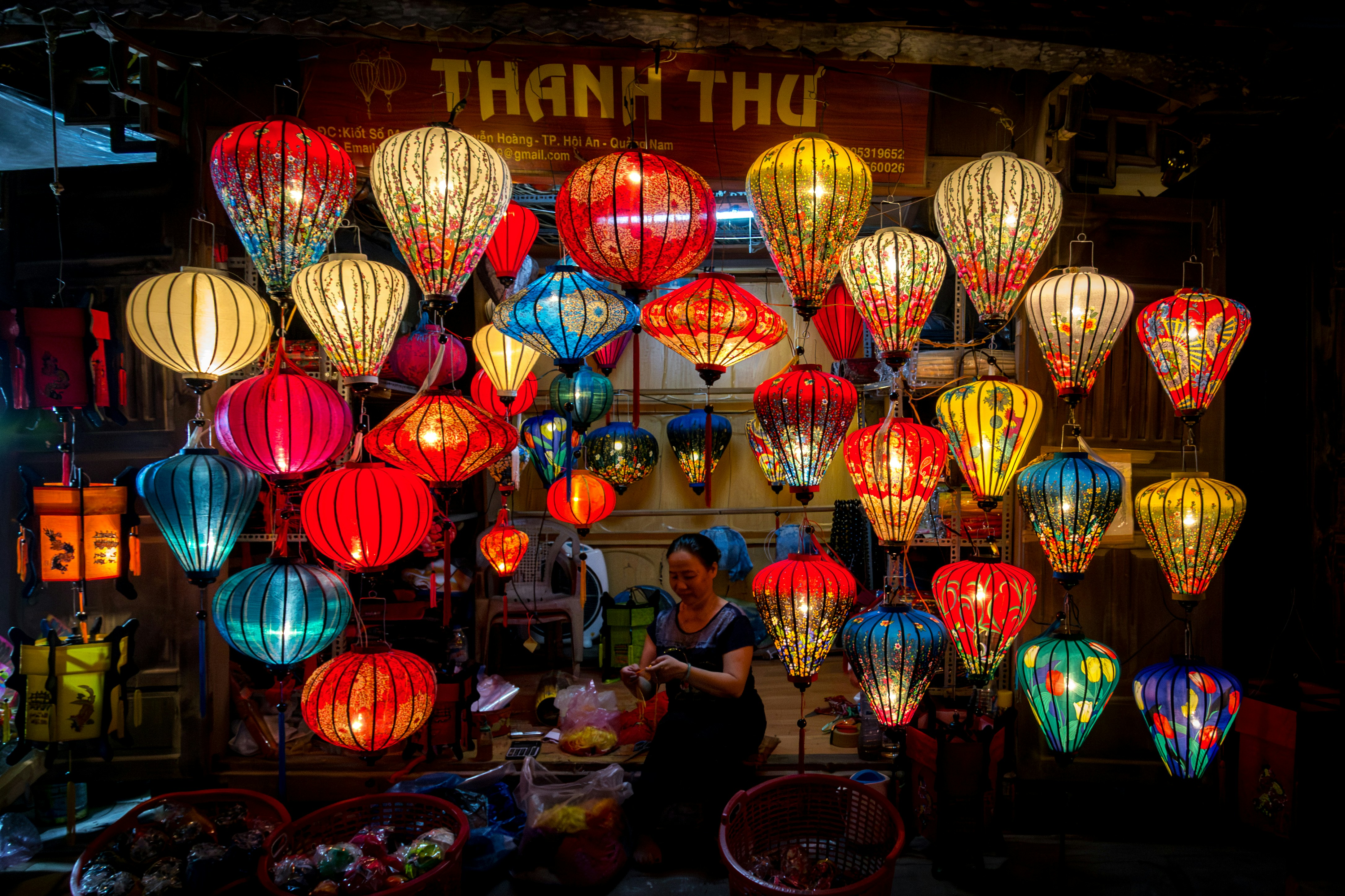 Colorful Lanterns at Night Market in Hoi An, Vietnam. A vibrant display of traditional lanterns in Hoi An, Vietnam. Their glowing colors illuminate the night and reflect the charm of this ancient town. | Colorful lanterns illuminate a night market with people browsing