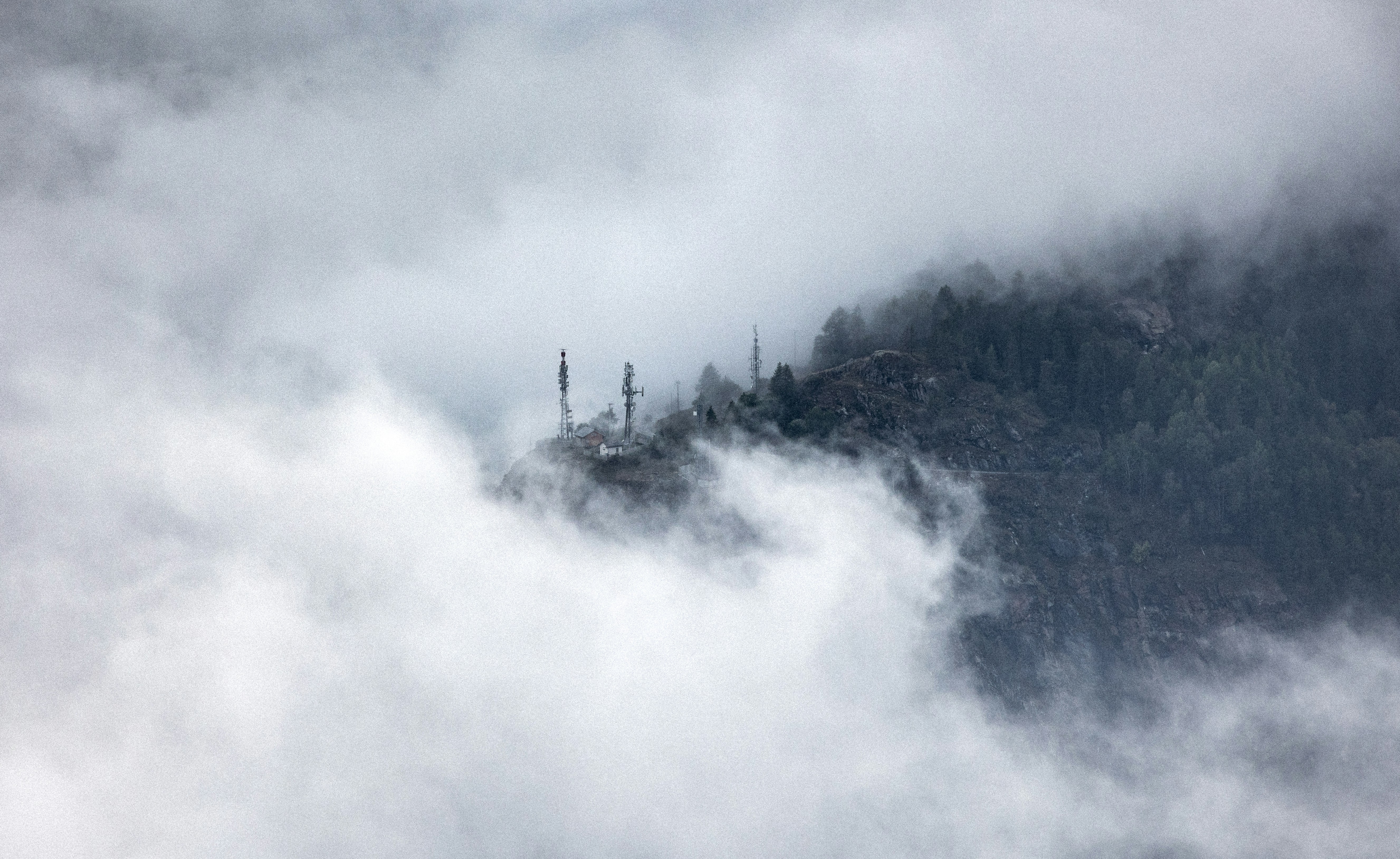 Telecommunication towers emerge from a blanket of fog on a rocky mountain, symbolizing the intersection of nature and technology.