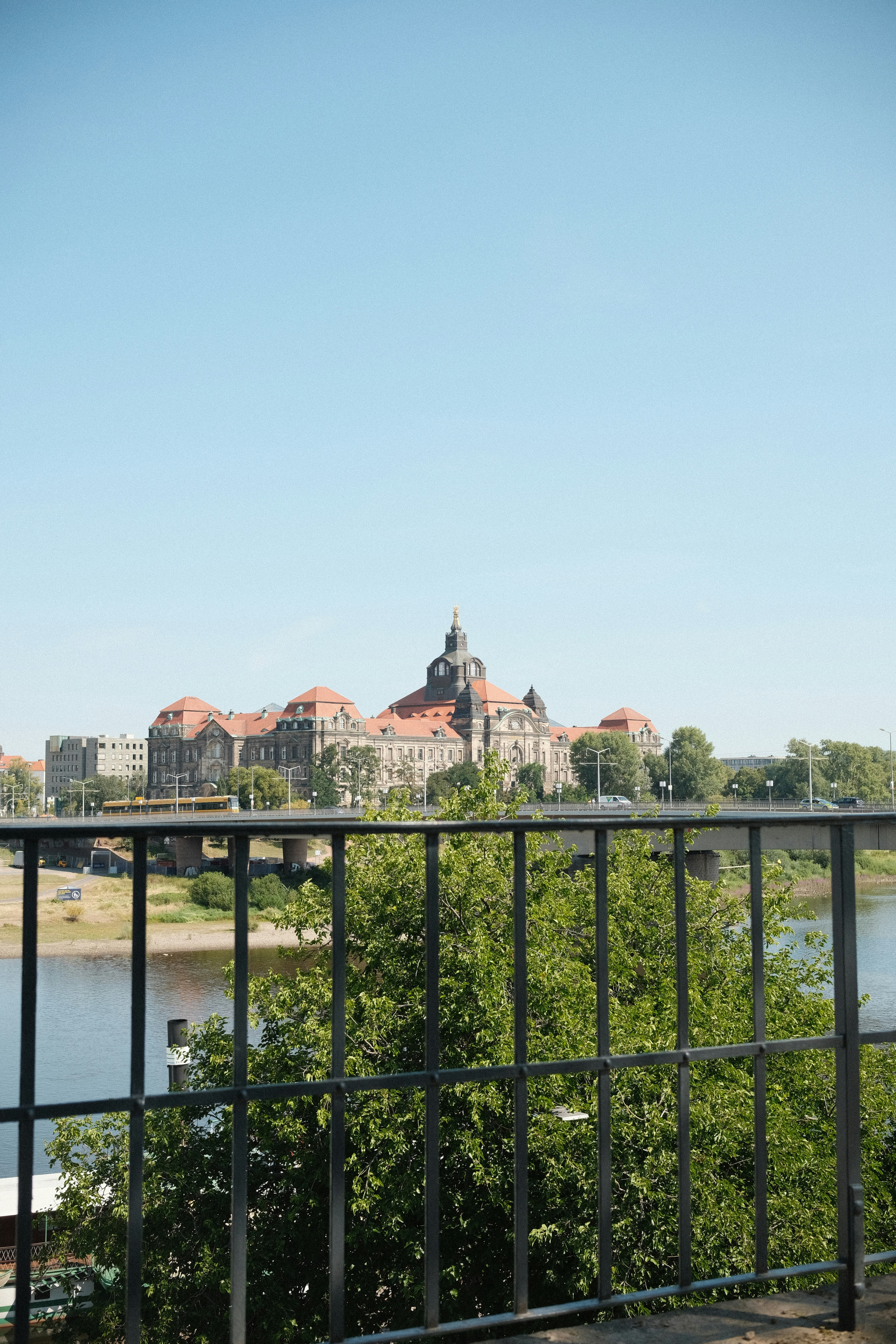 Historic building on a river with trees and railing.