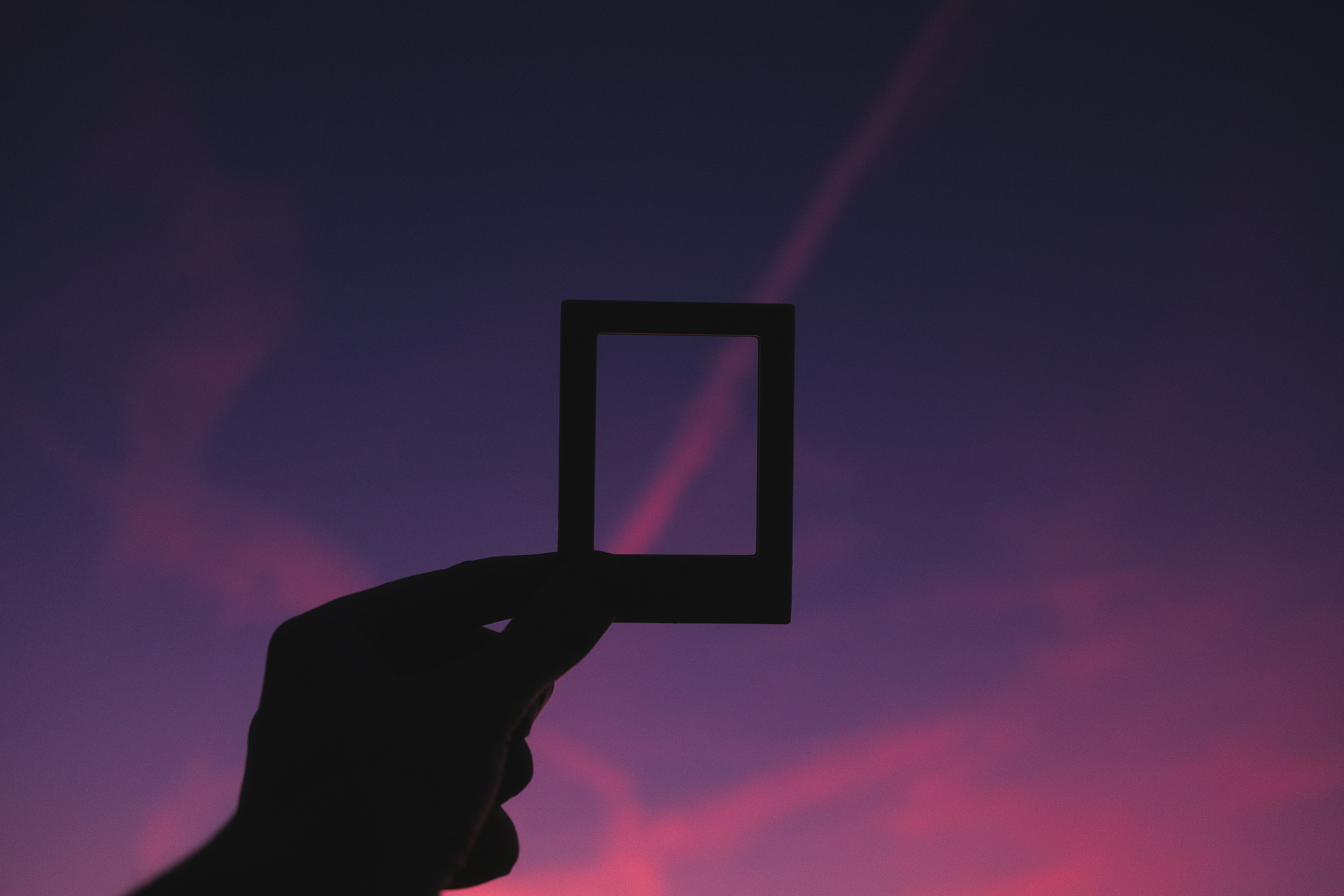 Hand holding frame against colorful sunset sky