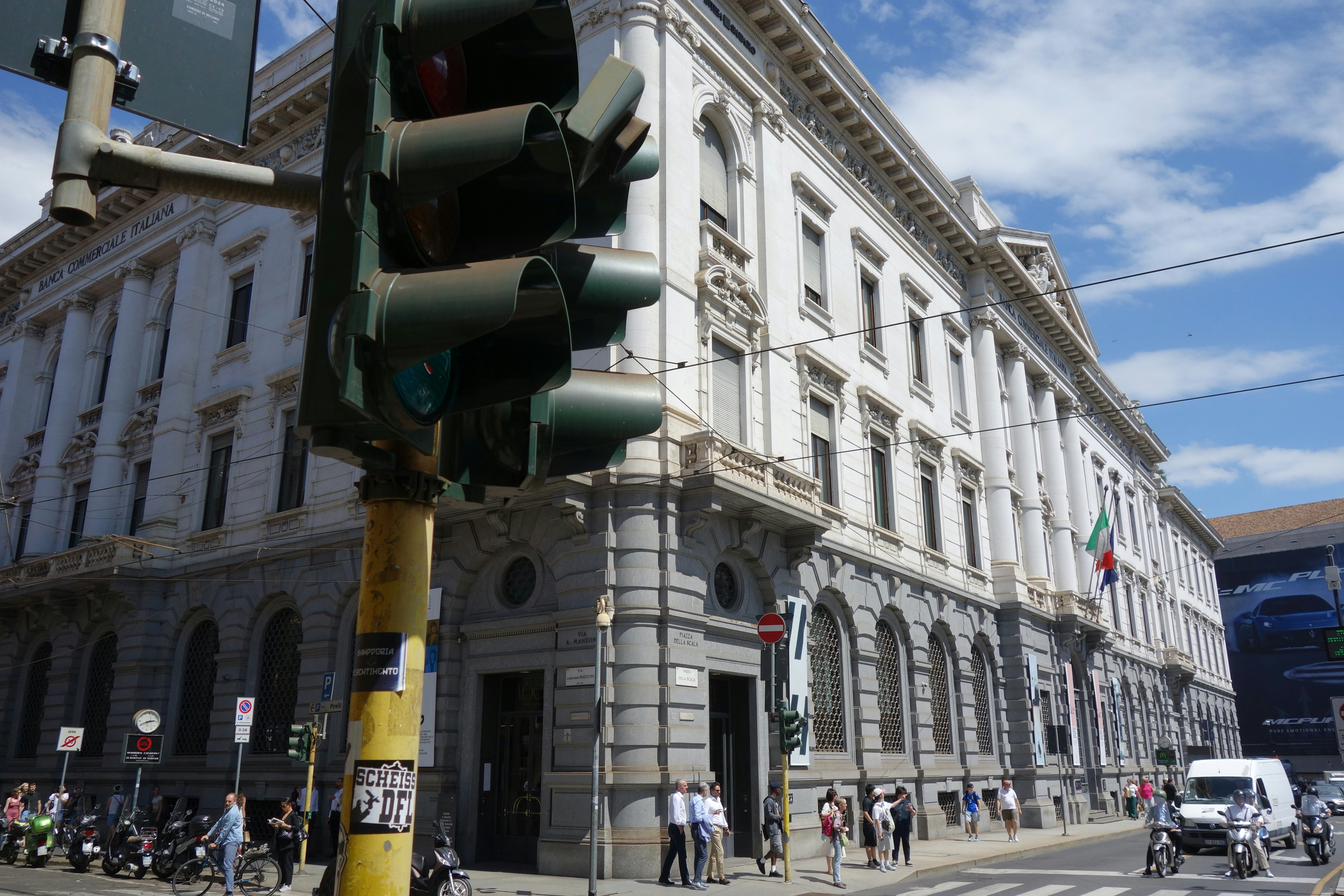 A historic building stands prominently at a busy intersection, complemented by a traffic light and pedestrians going about their day.