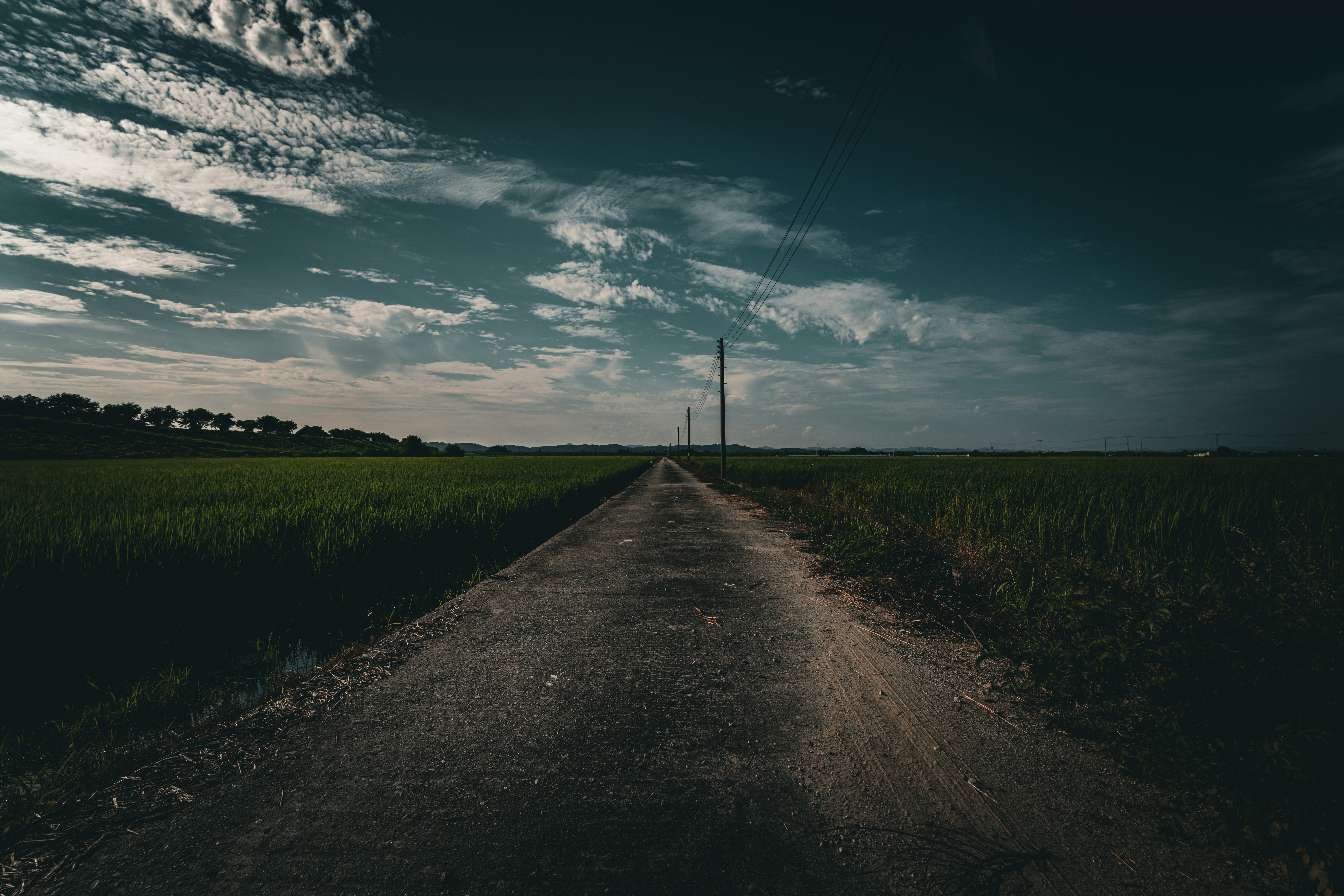 A long, empty road through green fields under a cloudy sky.