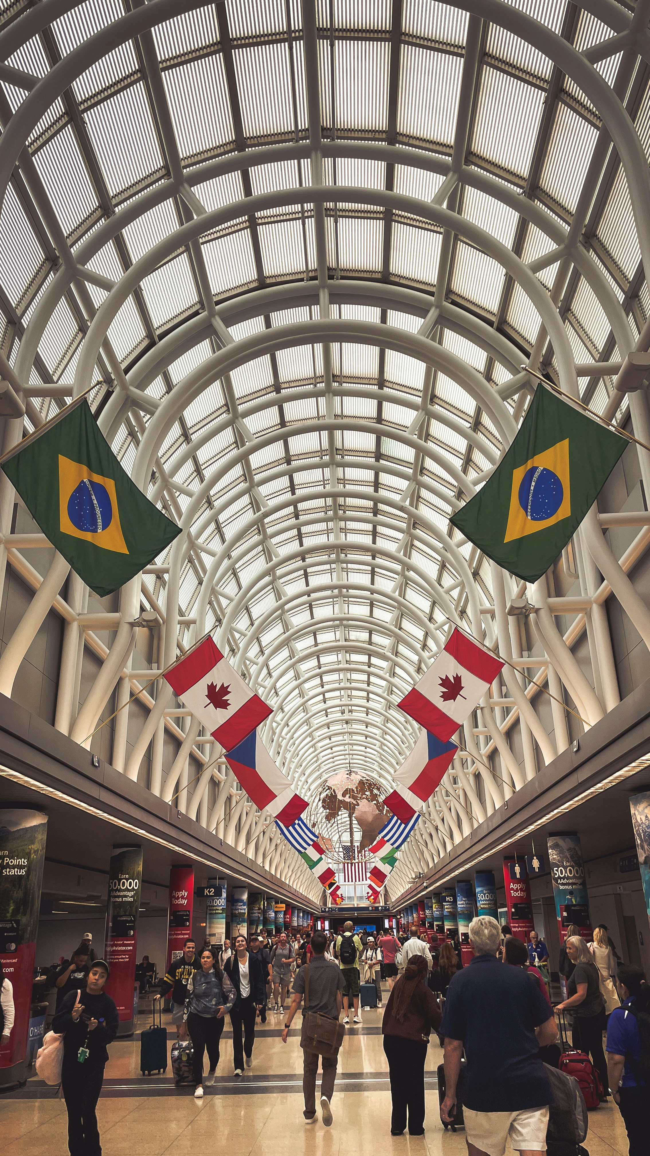 People walk through an airport concourse with flags hanging