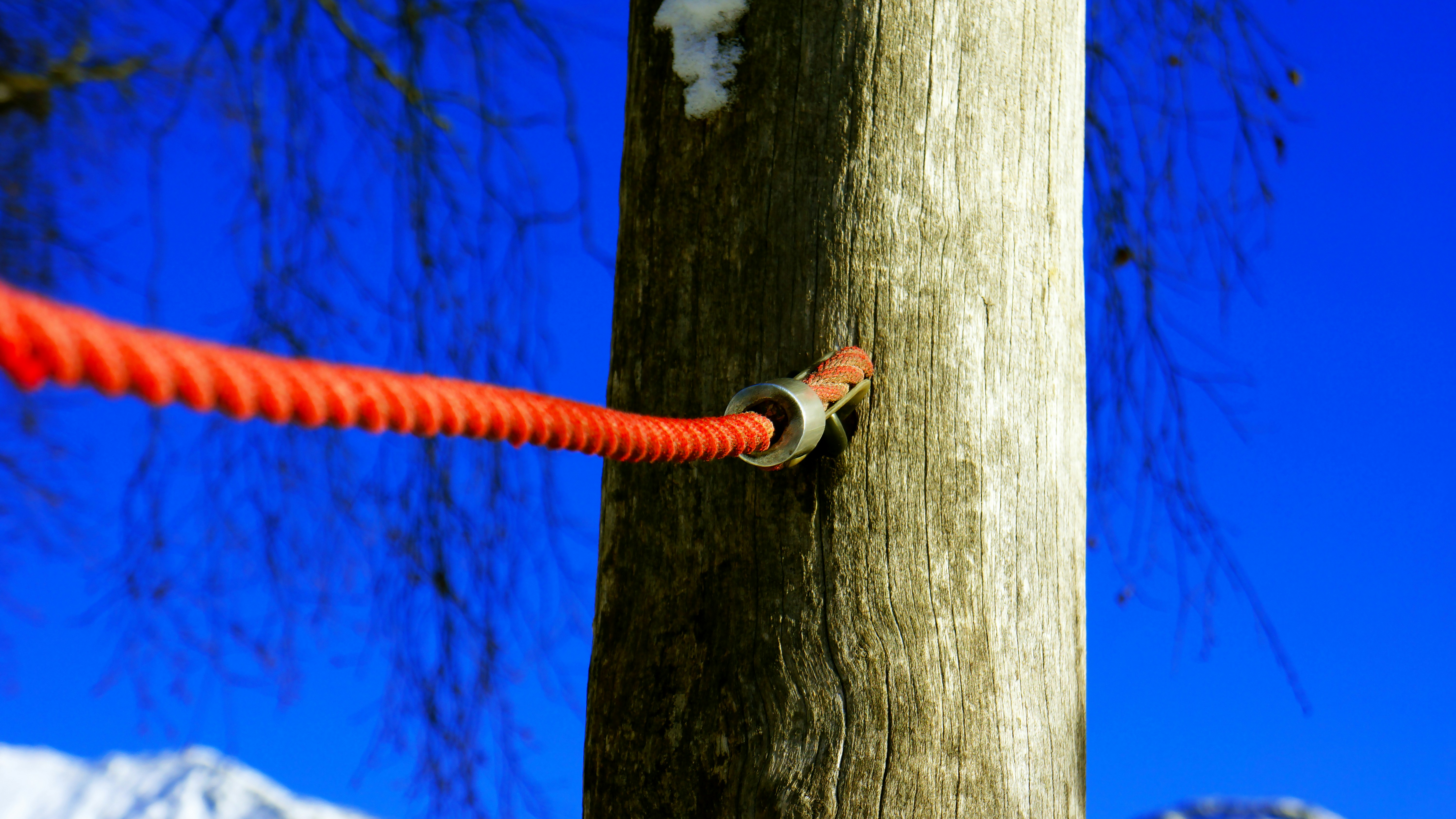 Red rope attached to wooden post against blue sky