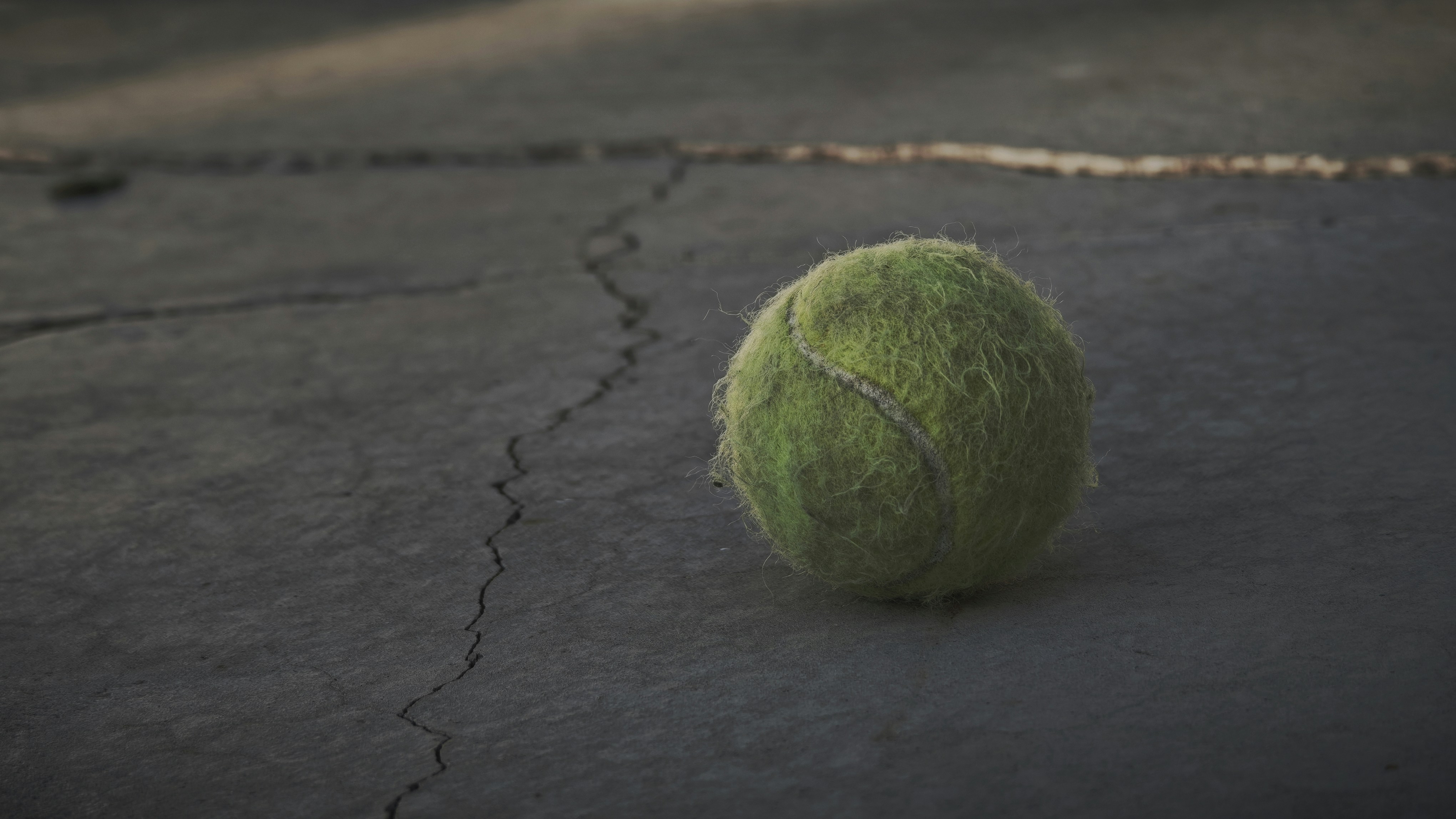 Worn tennis ball rests on cracked concrete surface, hinting at stories of play and abandonment.