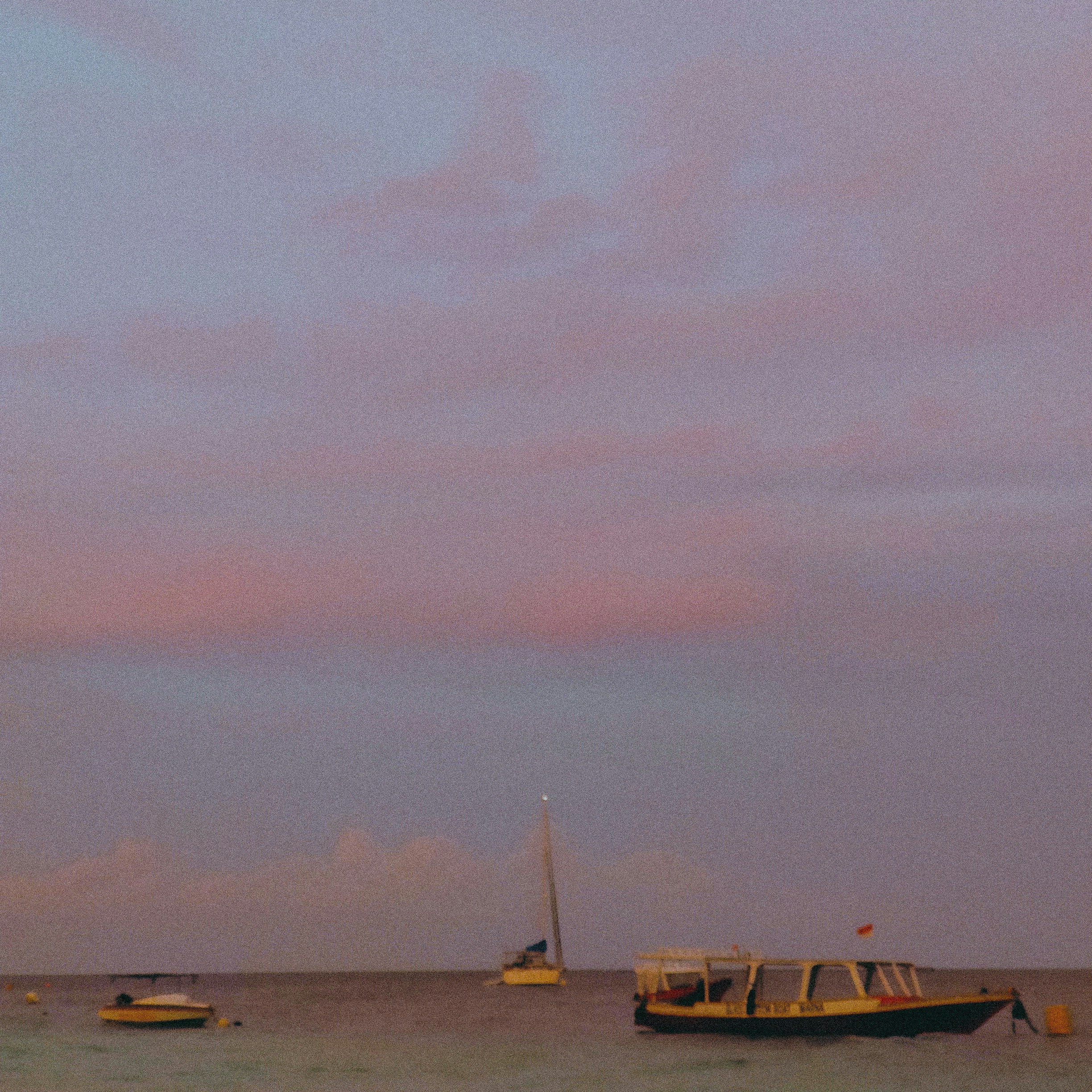 Boats float on the ocean under a pastel sky.