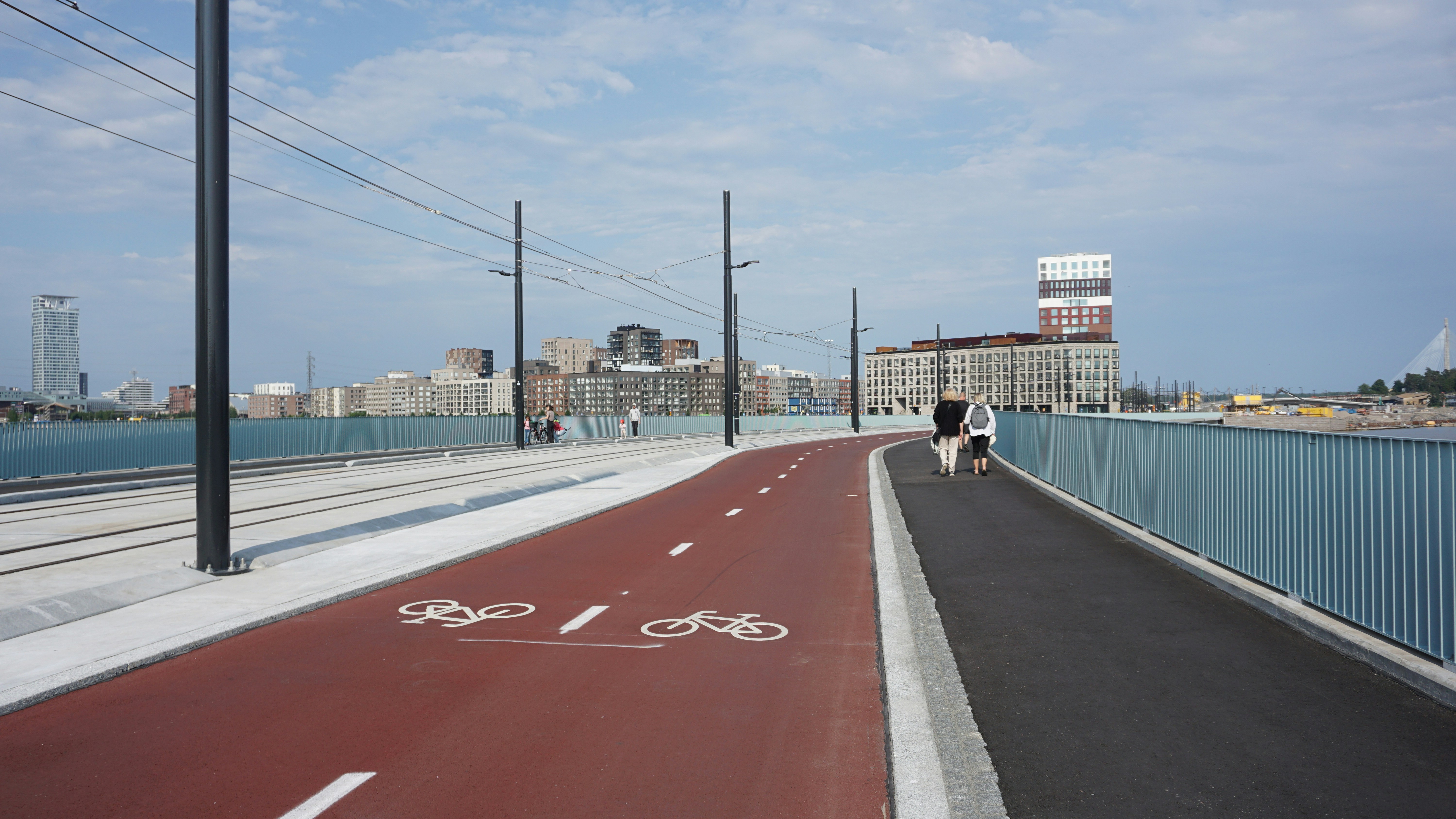 A dual-purpose pathway in an urban setting, featuring distinct lanes for cyclists and pedestrians, flanked by city buildings under a clear sky.