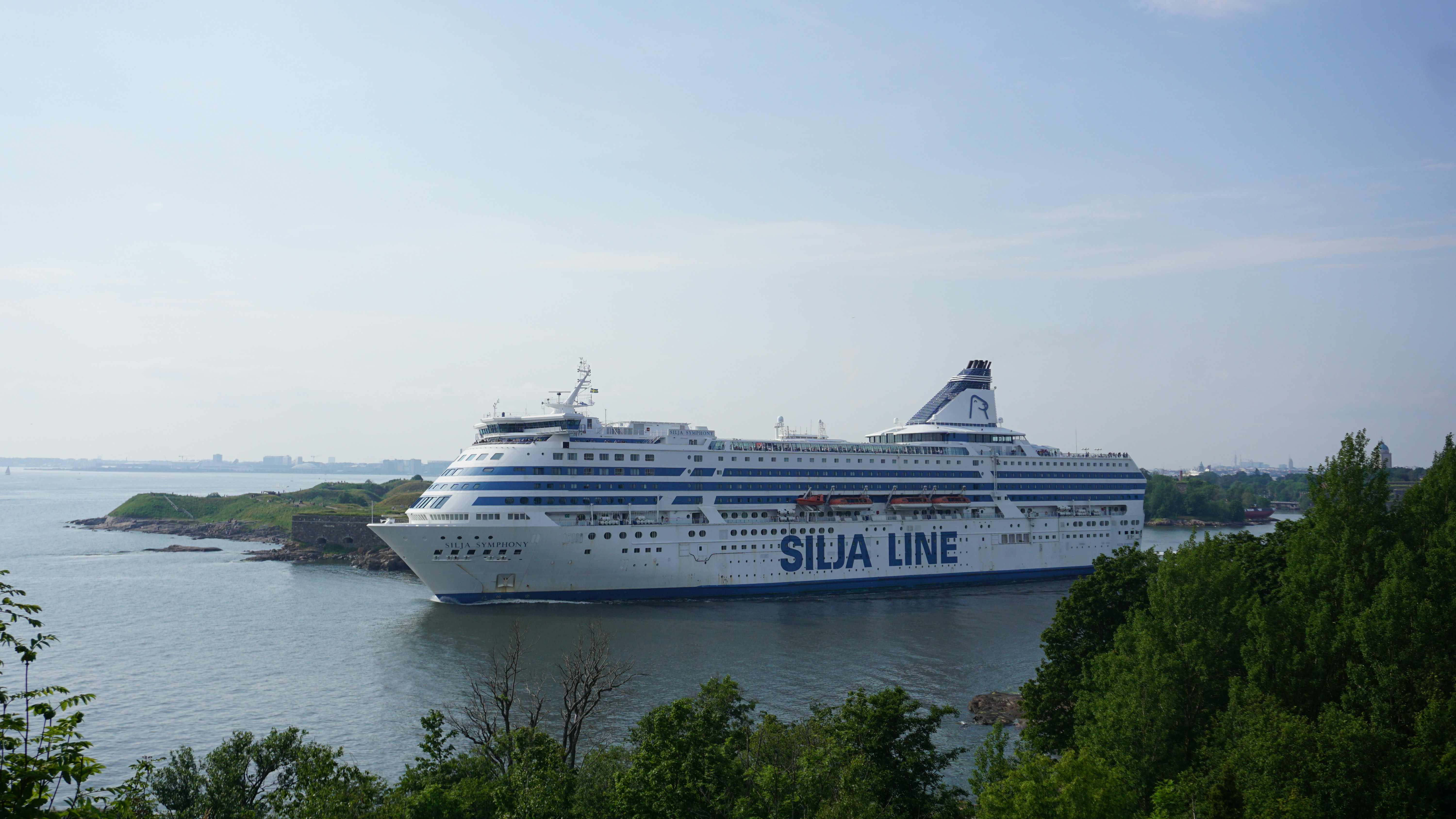 A Silja Line cruise ship glides through calm waters, framed by lush greenery and distant islands. The scene captures the essence of maritime travel.