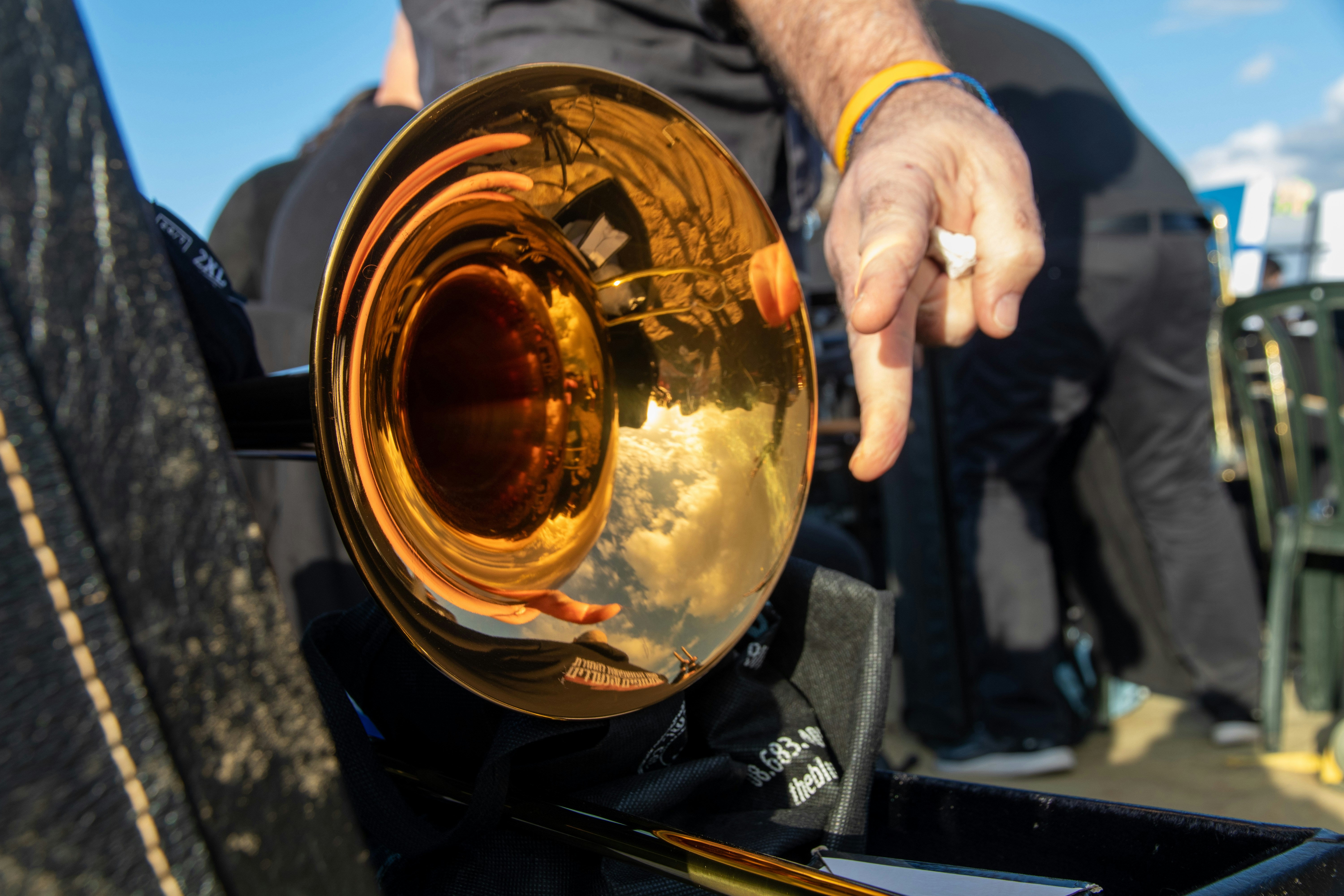 Shiny brass instrument reflecting a vibrant sky and surroundings, with a hand poised nearby. The scene captures the essence of musical preparation.