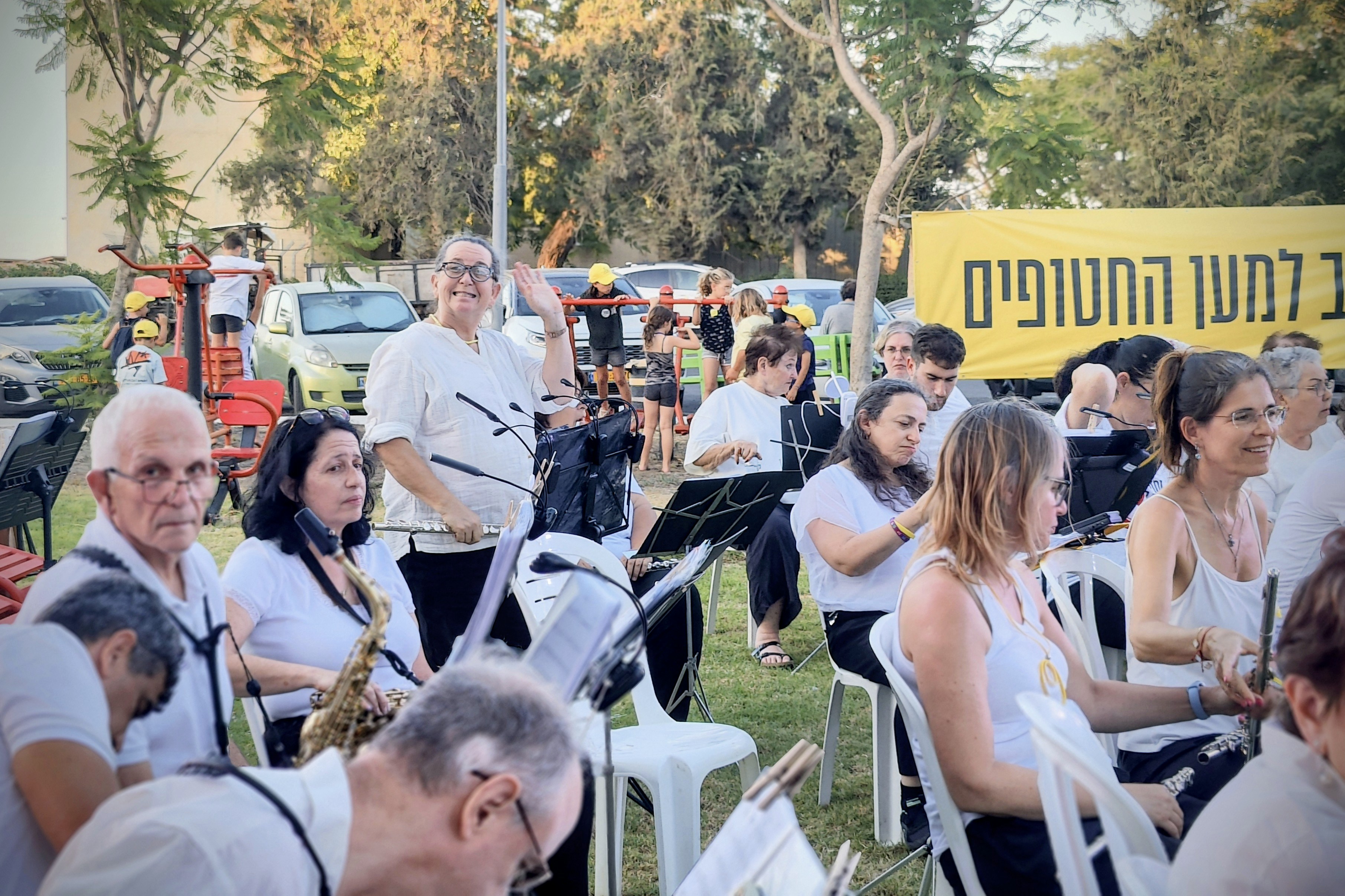 An outdoor orchestra performs with audience members watching. photo ...