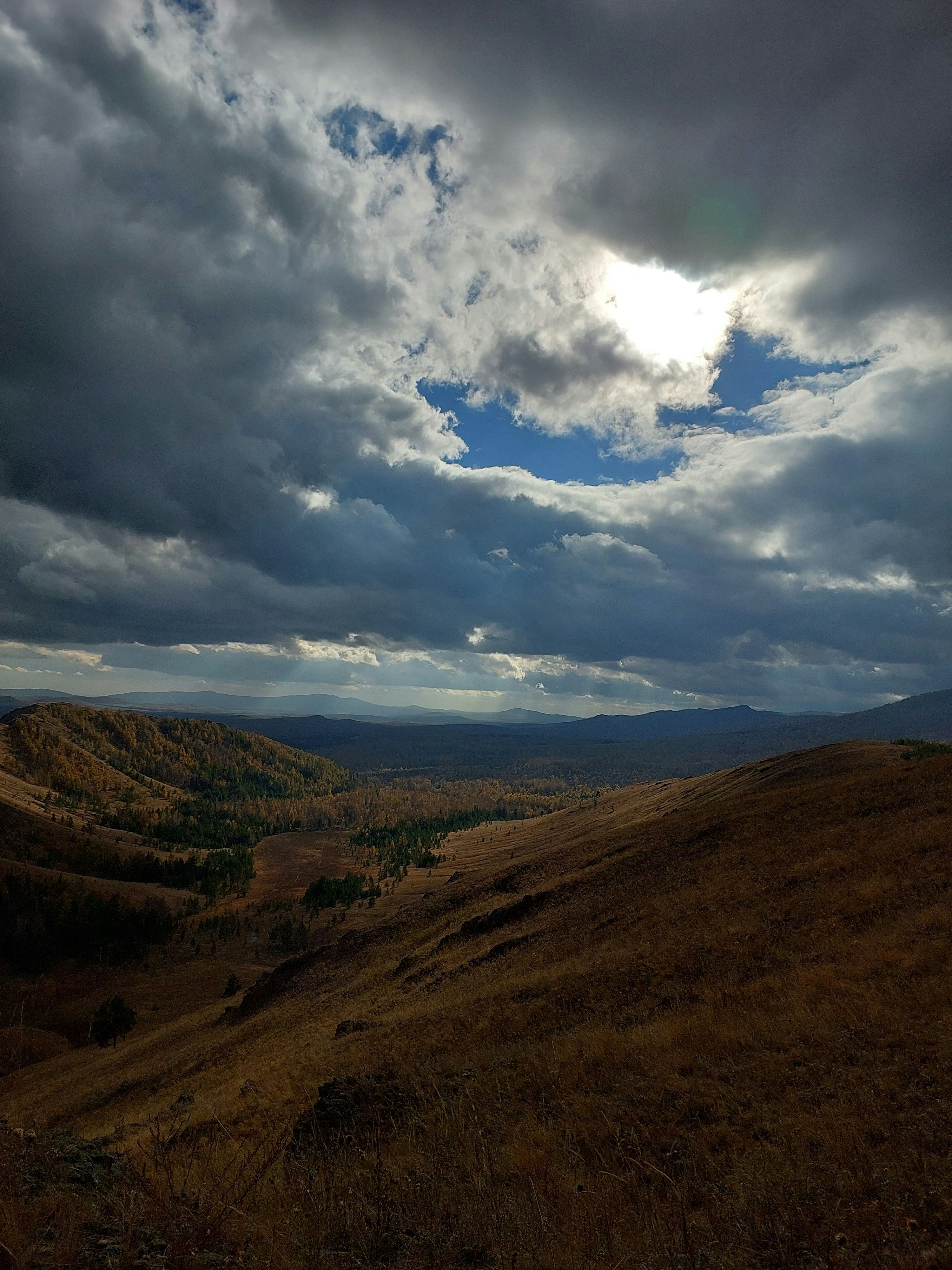 Dramatic clouds loom over a golden-hued valley, capturing the essence of autumn's transition. The interplay of light and shadow enhances the landscape's depth.