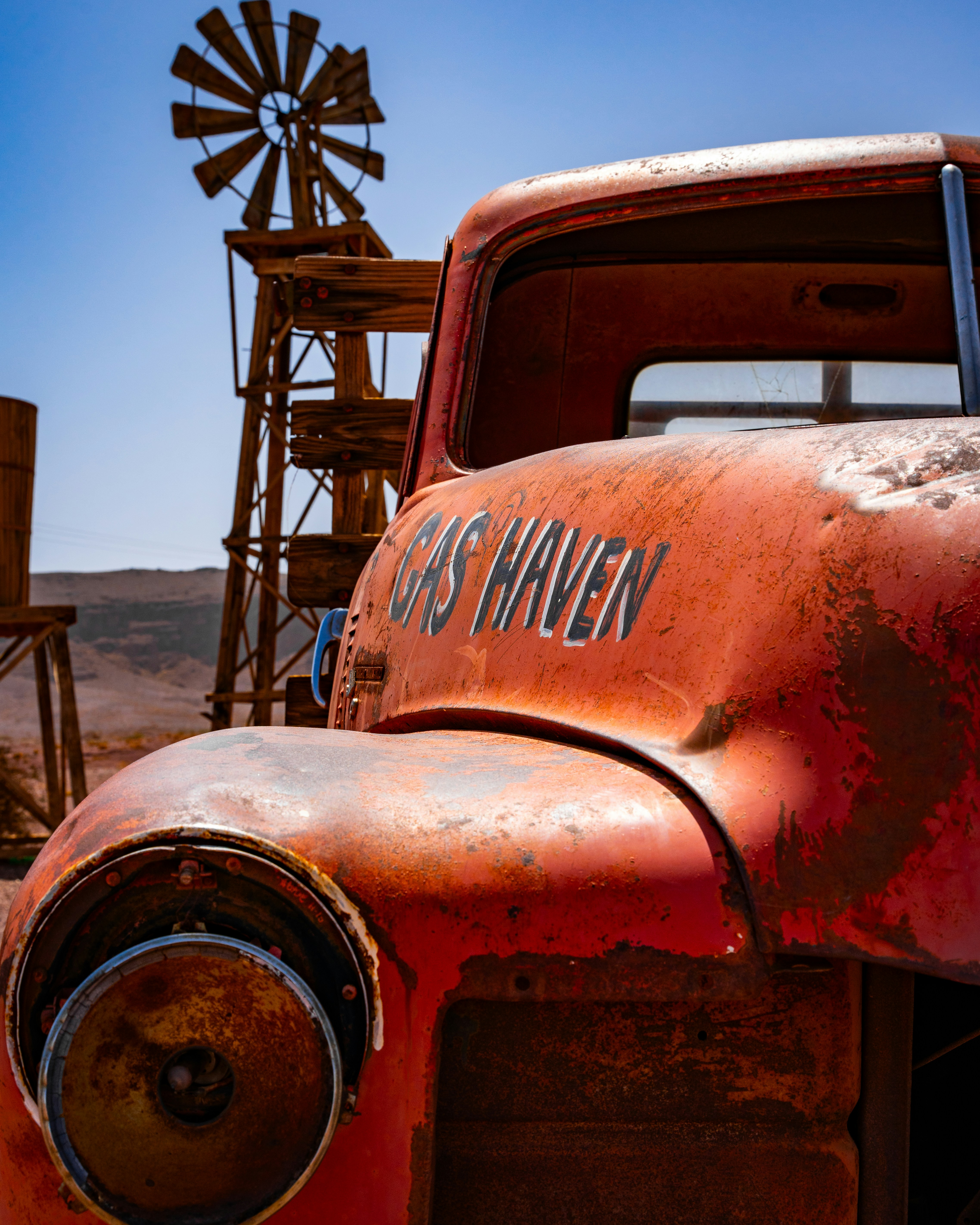 Old orange truck car at the iconic filming location of the movie "The Hills Have Eyes" in Ouarzazate, Morocco. | Rusty vintage truck with windmill in desert landscape.