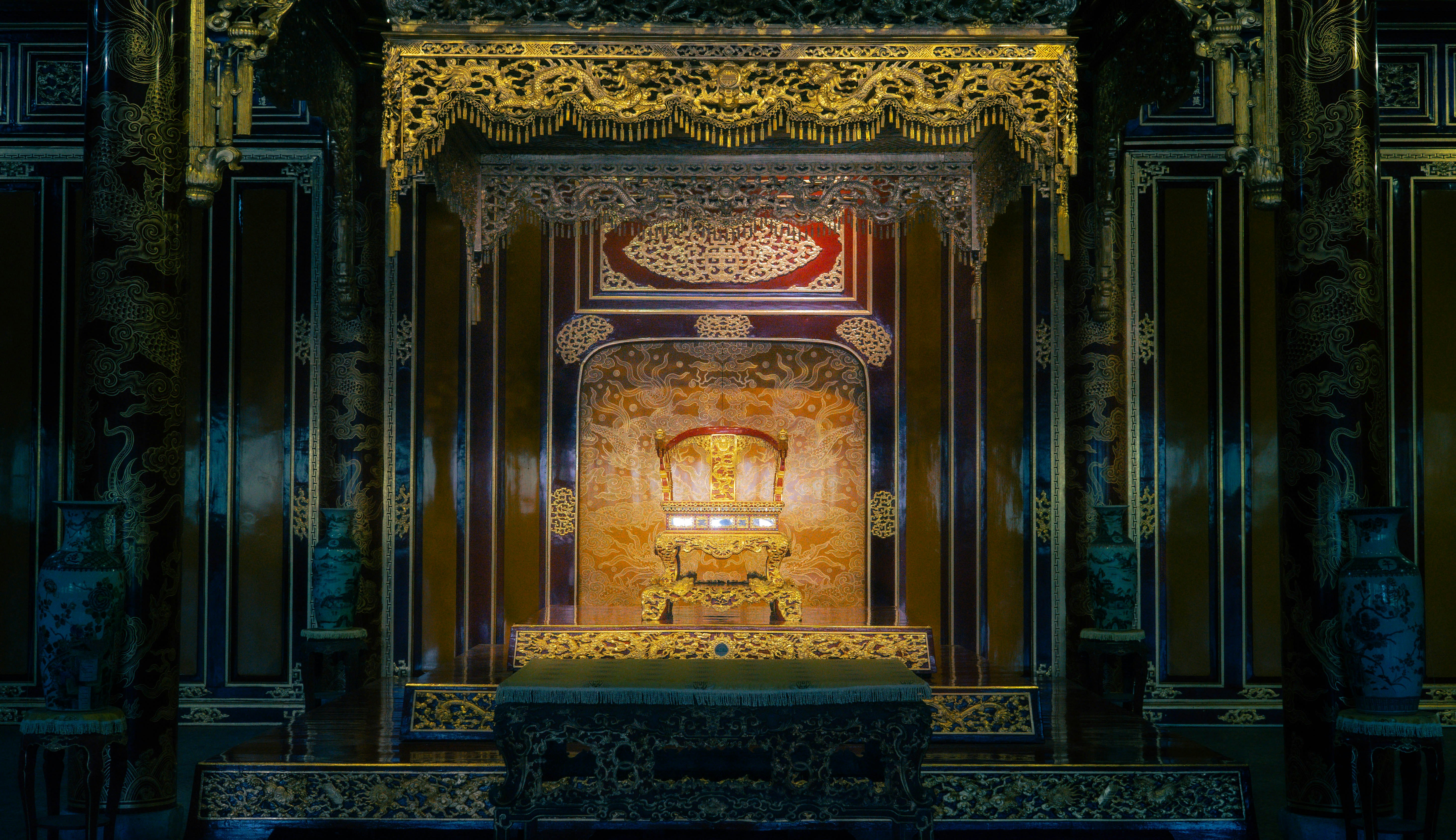 Intricately carved throne set against ornate walls in a dimly lit royal chamber.