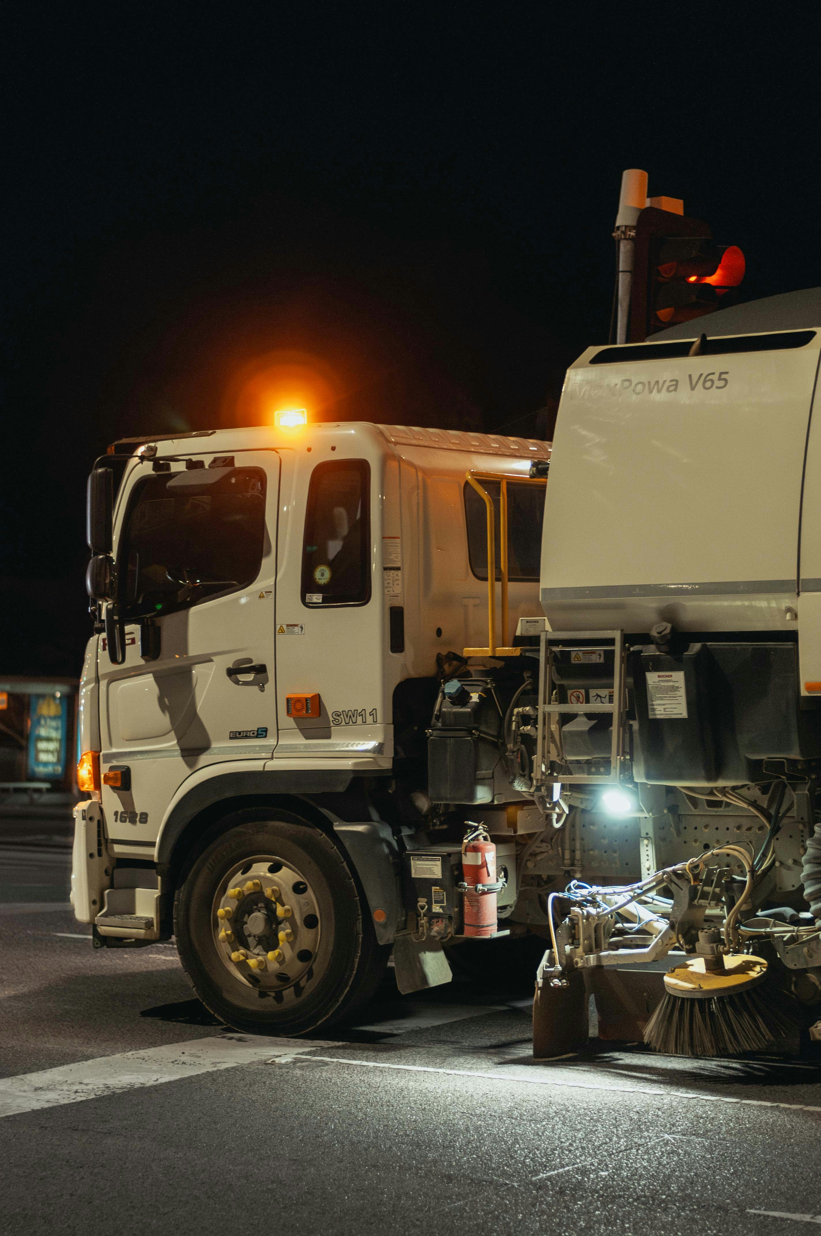 Street cleaning truck illuminated by its own lights, actively maintaining urban cleanliness at night.