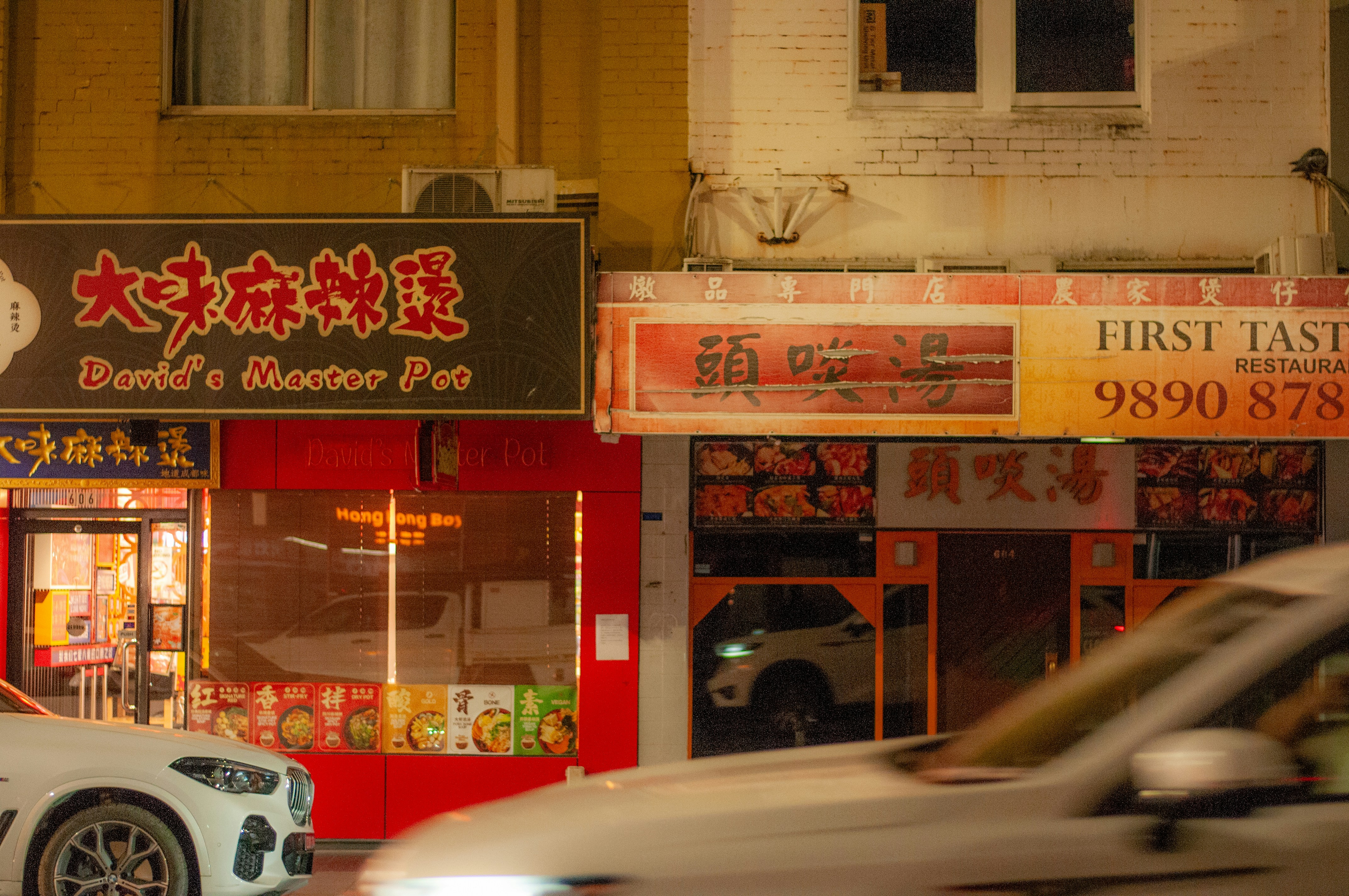 Vibrant storefronts of Asian restaurants illuminated at night, showcasing colorful signage and inviting atmospheres.