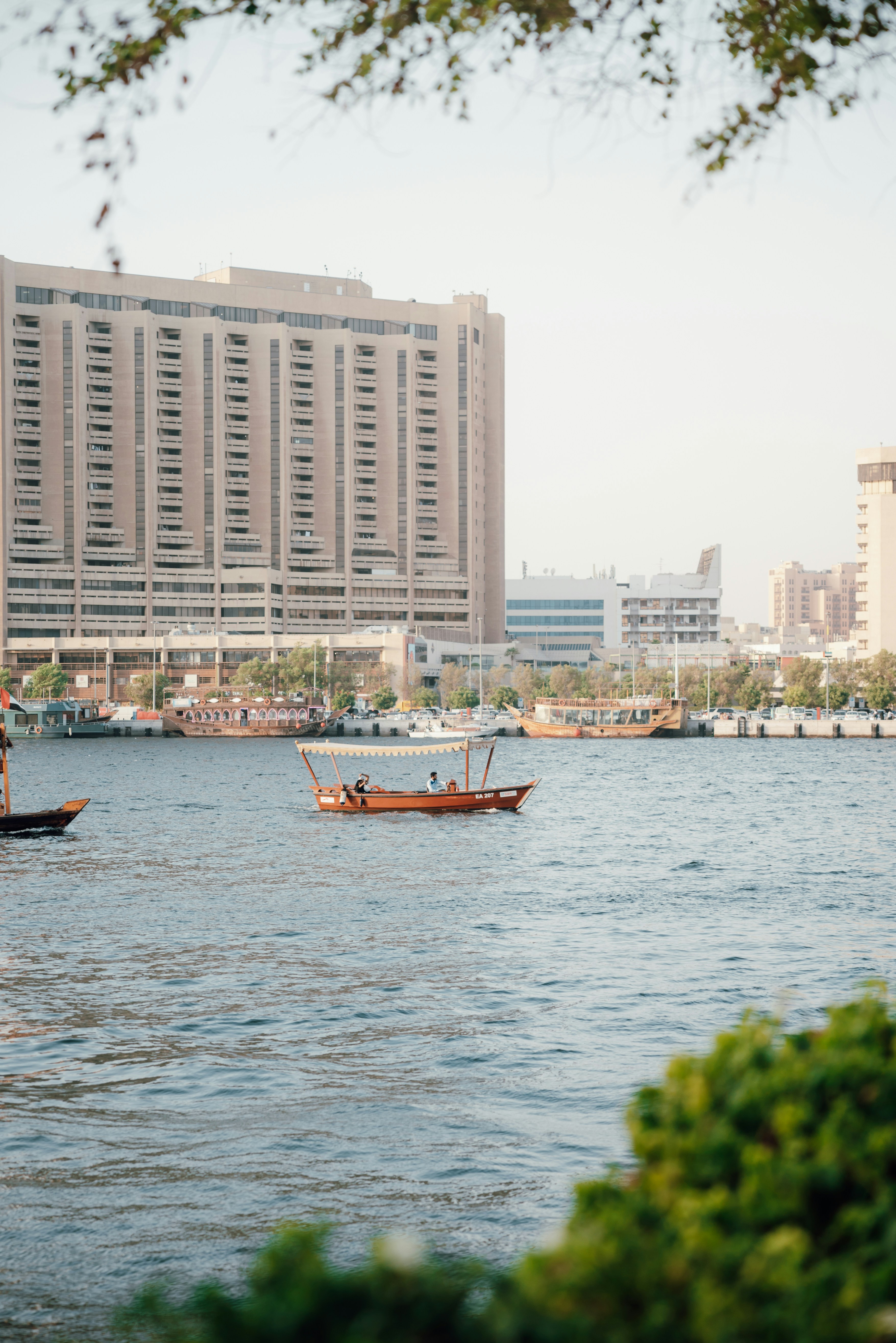 Traditional wooden boats glide along a serene waterway, framed by modern high-rise buildings. The scene captures the juxtaposition of nature and urban life.