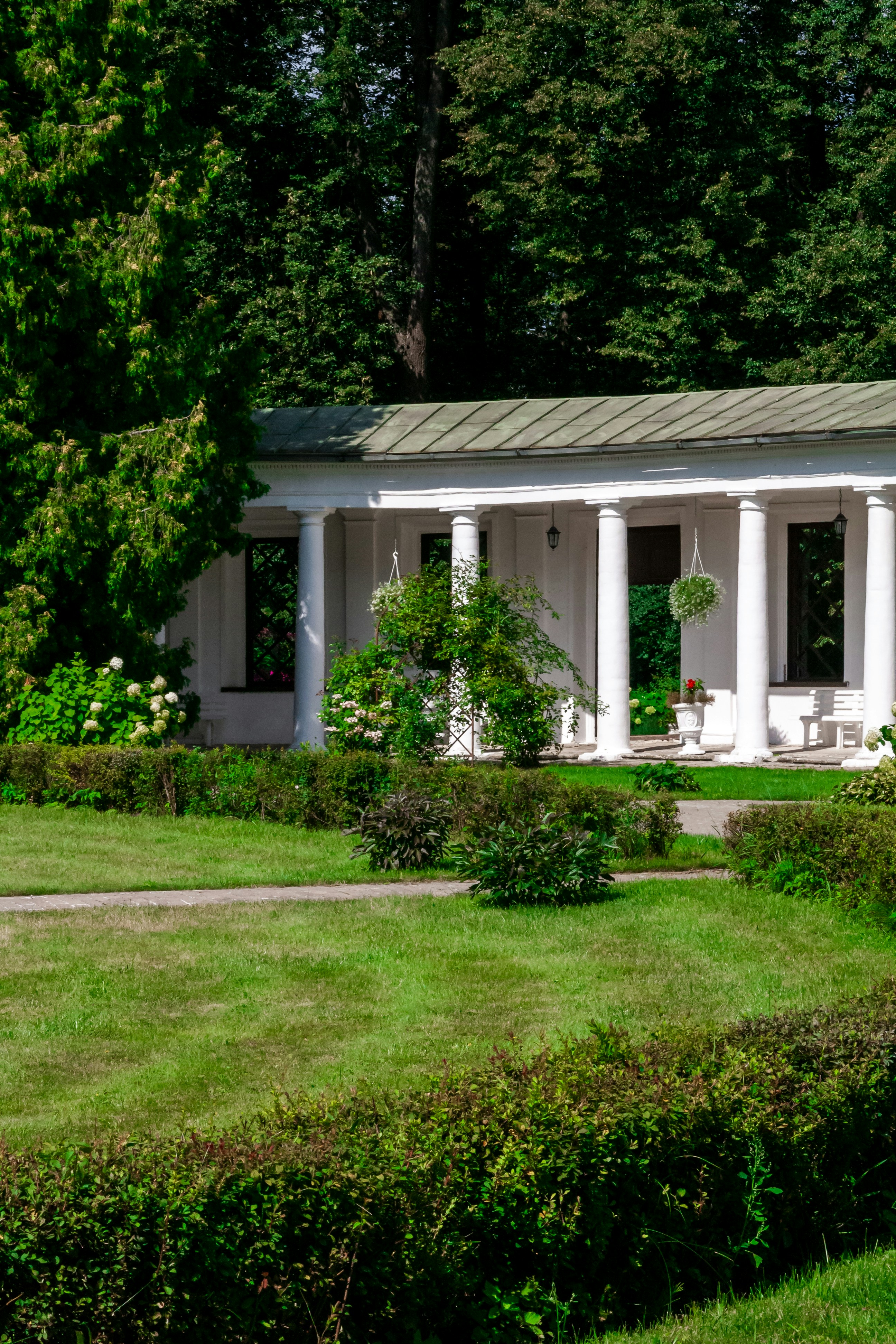 White building with columns in a lush garden.