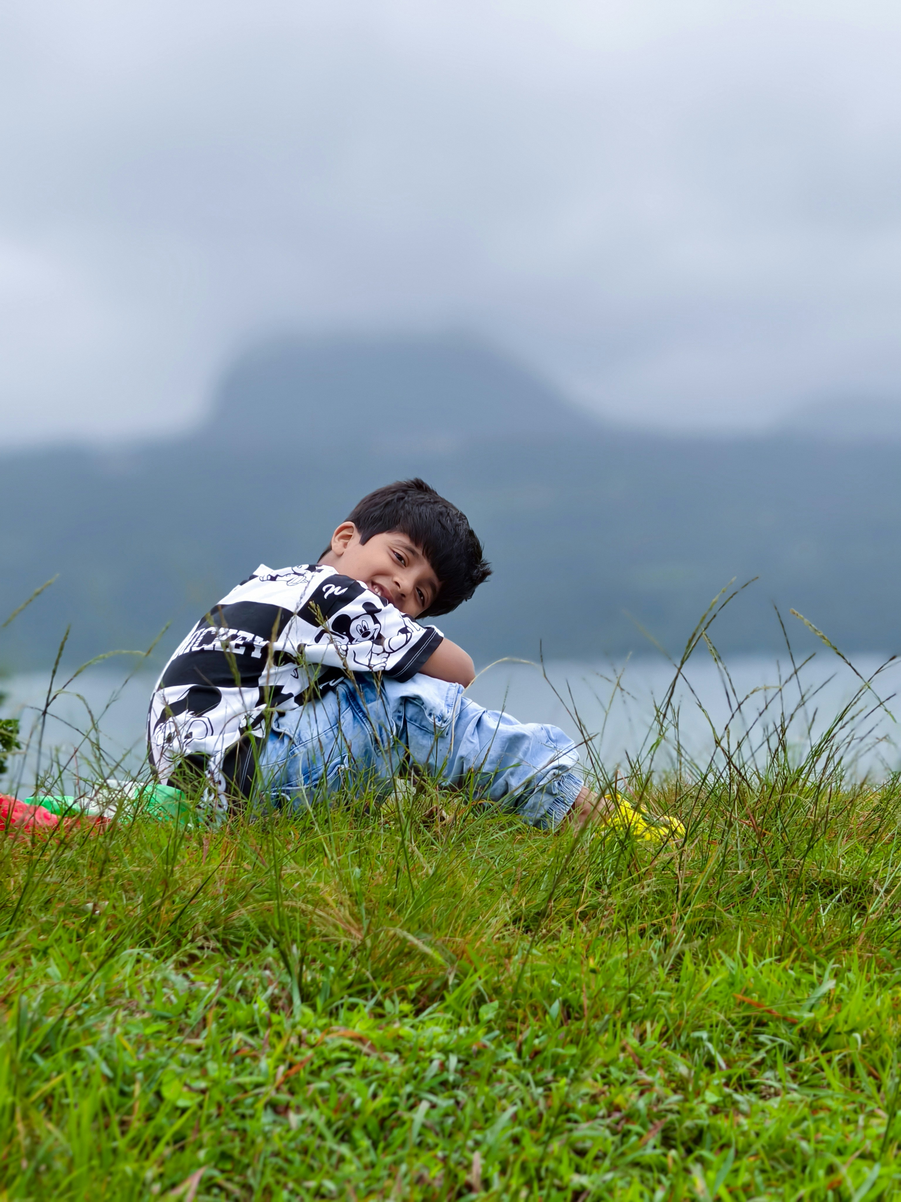 A young boy sits on grassy hill with mountains behind