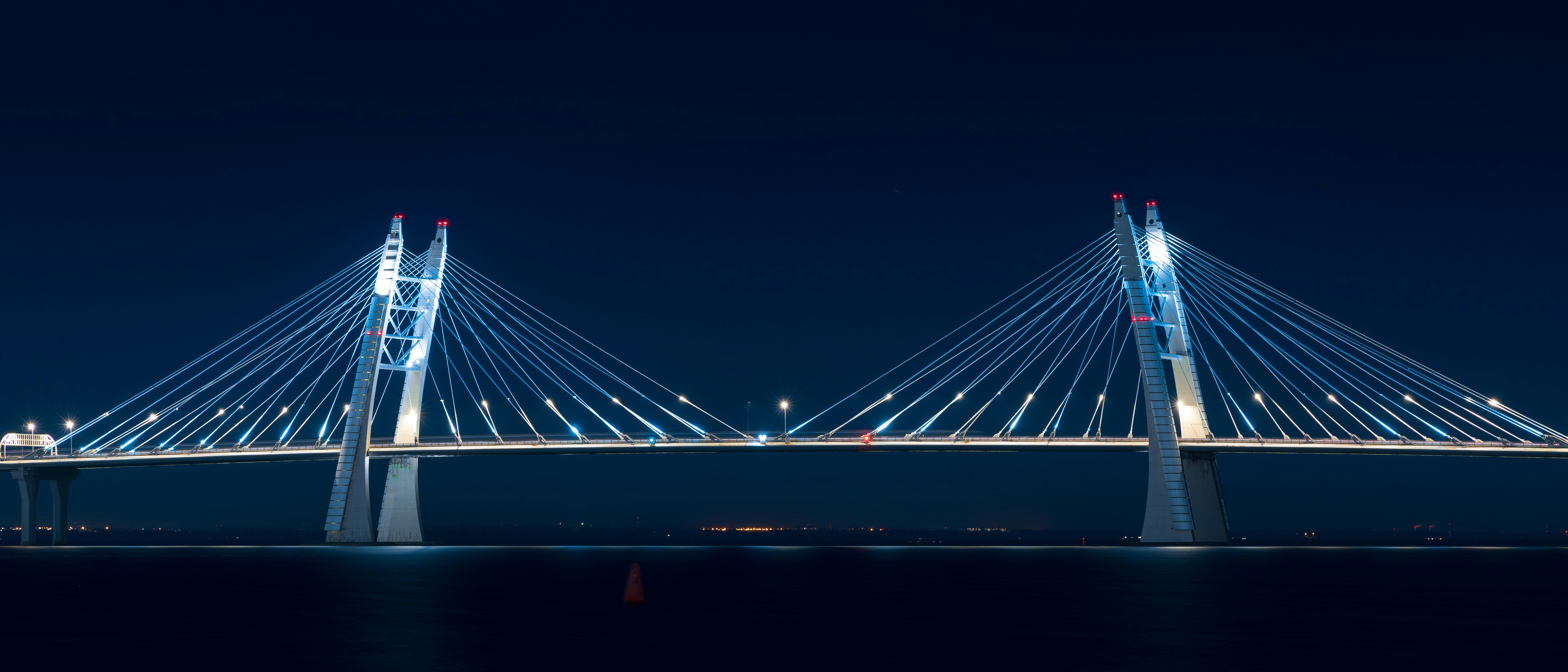 A modern suspension bridge illuminated against a dark night sky, showcasing intricate cable designs and architectural elegance.