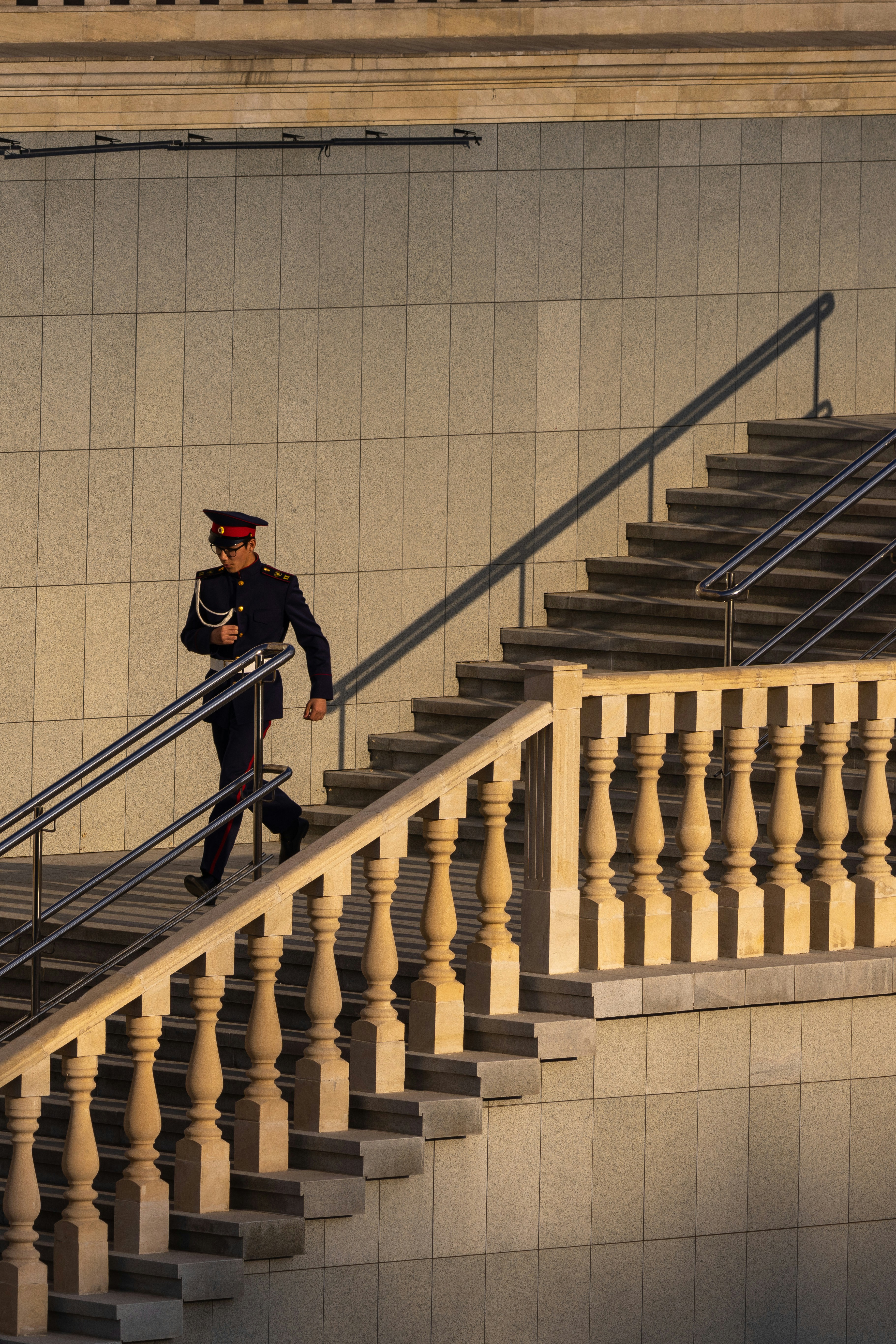 A uniformed officer descends a grand staircase, framed by elegant balustrades and warm golden light. The scene captures a moment of duty and architectural beauty.