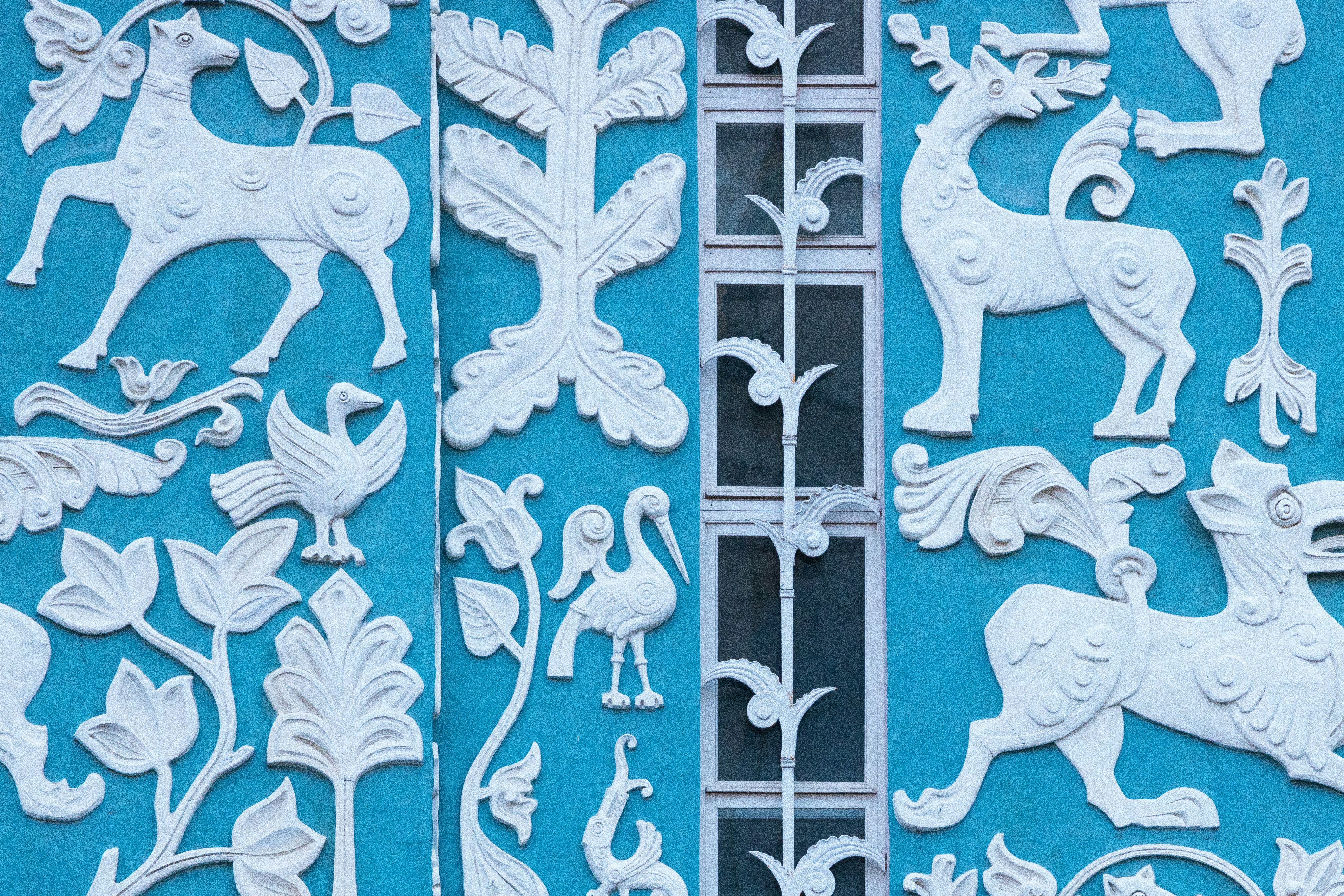 White relief ornaments of animals and plants on blue wall.