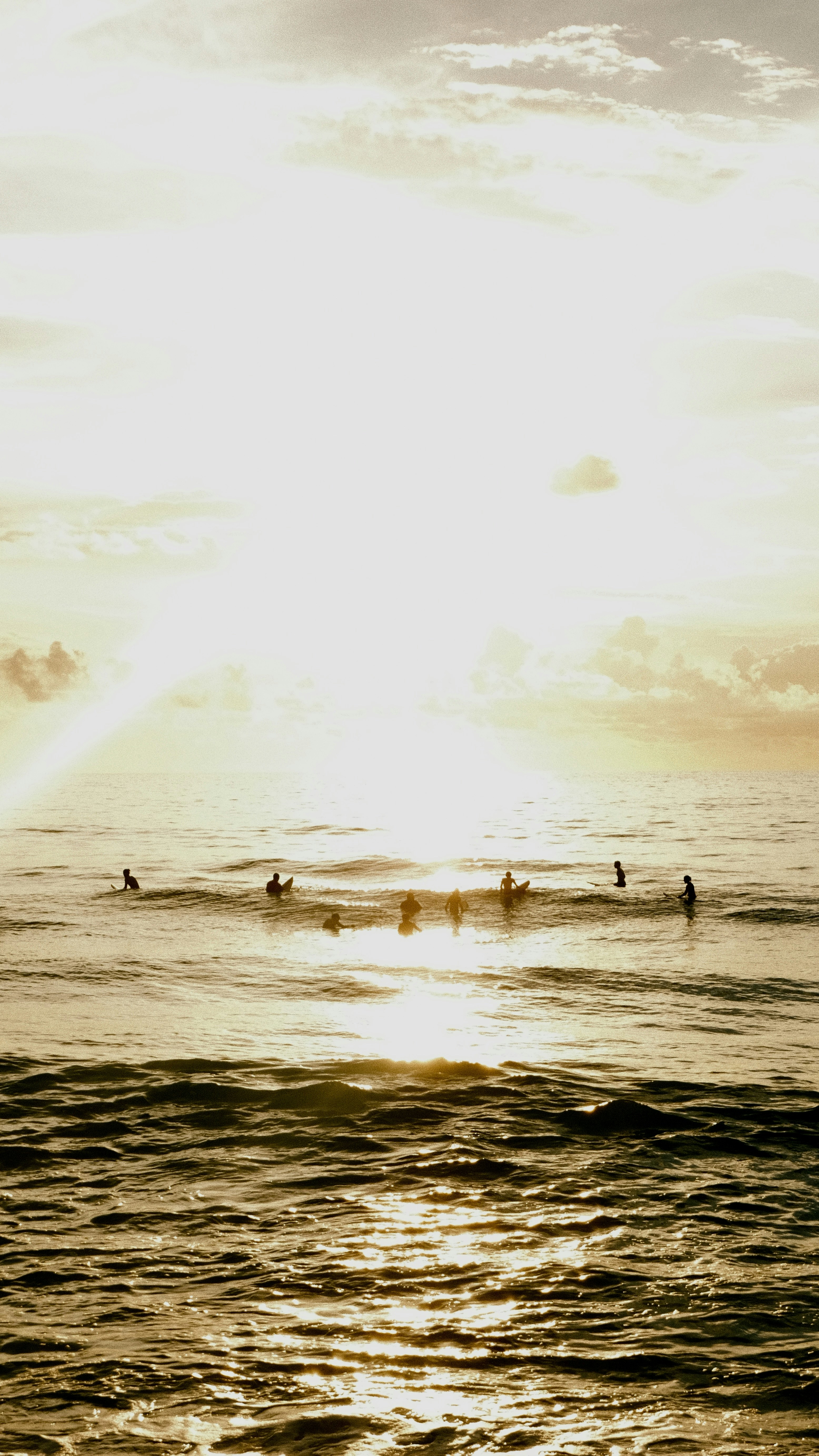 Surfers wait for waves at sunrise on the ocean.