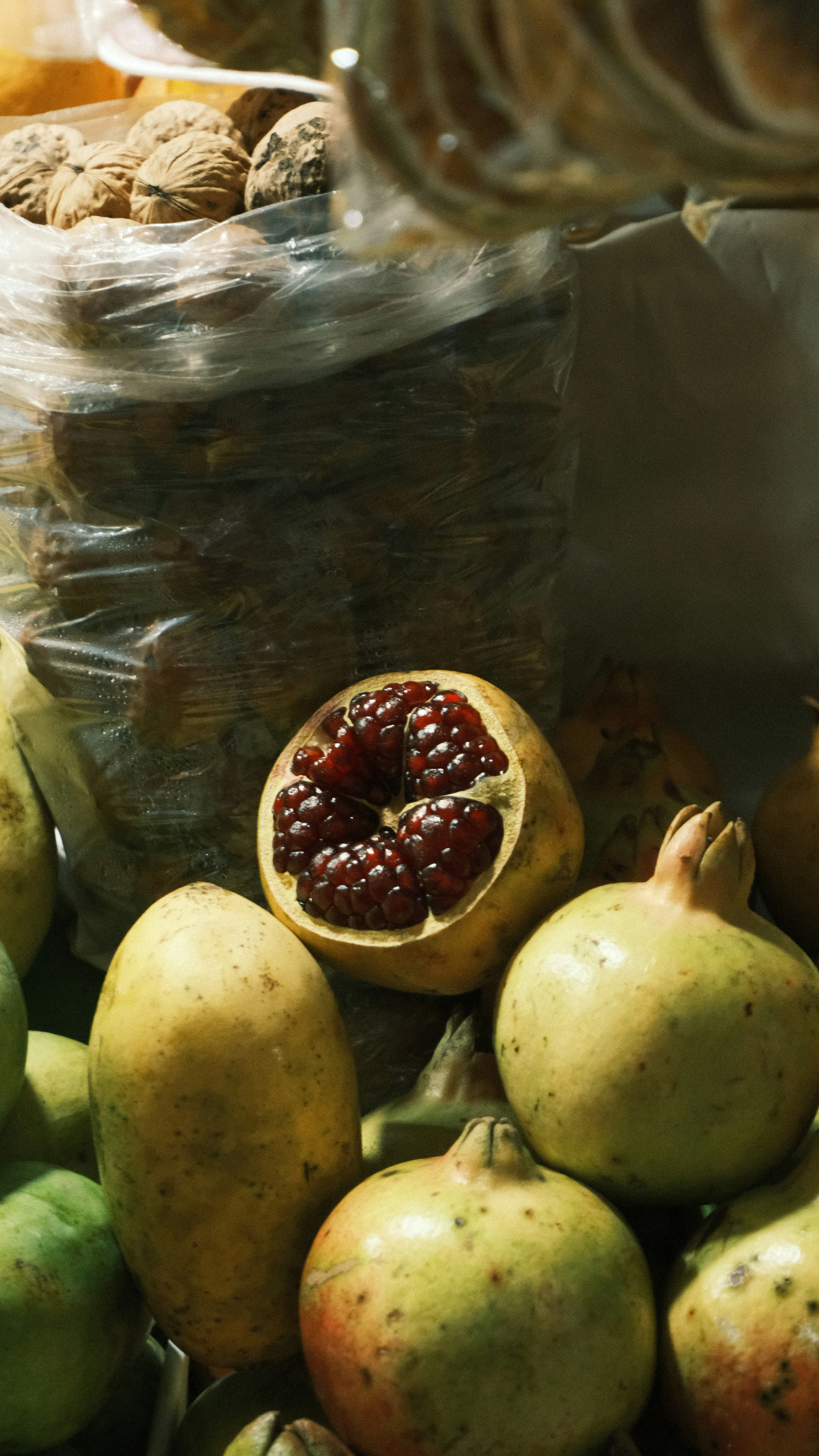A vibrant display of fresh fruits, featuring a cut pomegranate revealing its jewel-like seeds, surrounded by various other fruits. The scene captures the essence of a bustling marketplace.