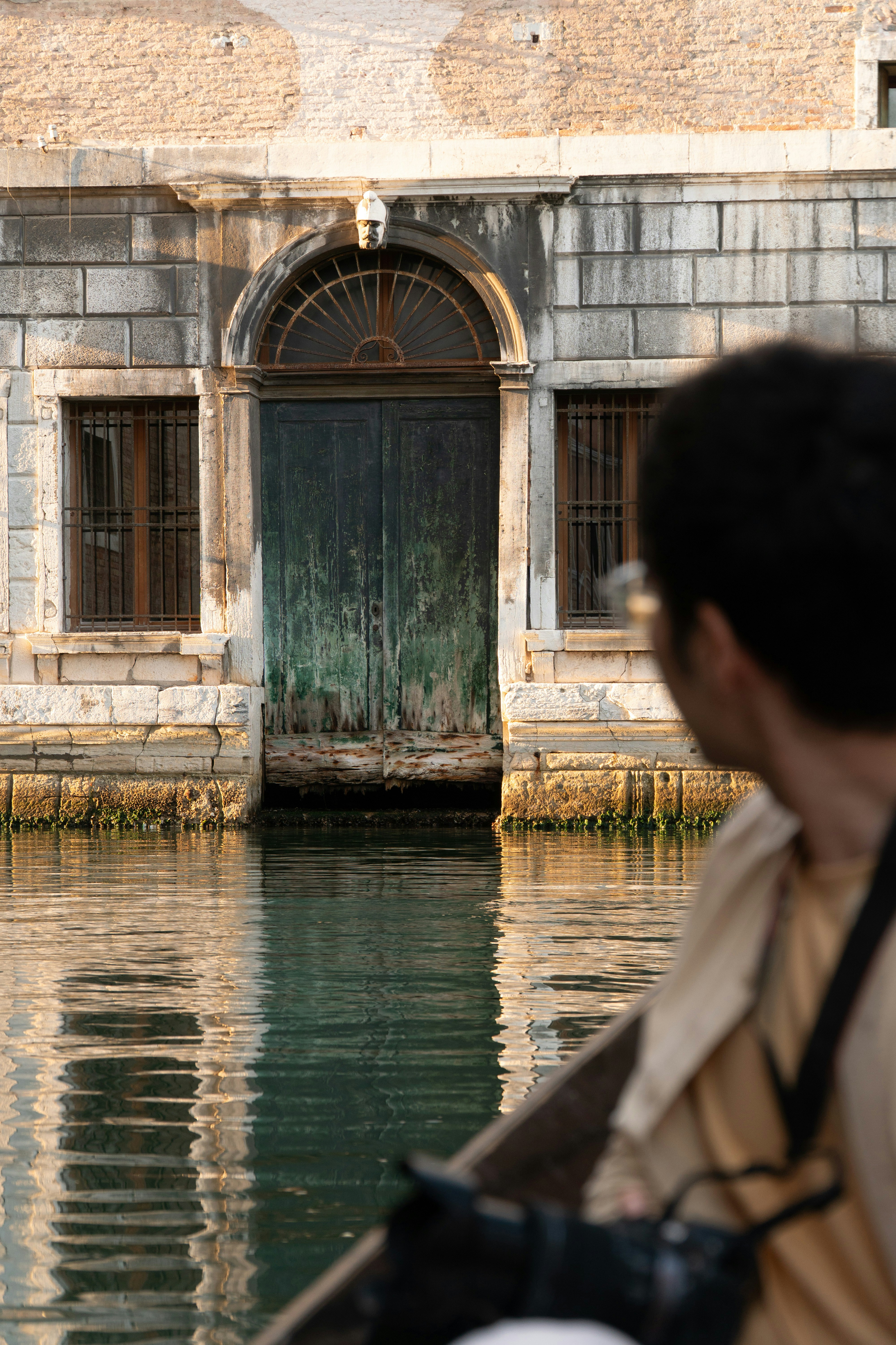 Weathered doorway over calm water, with a blurred observer in the foreground