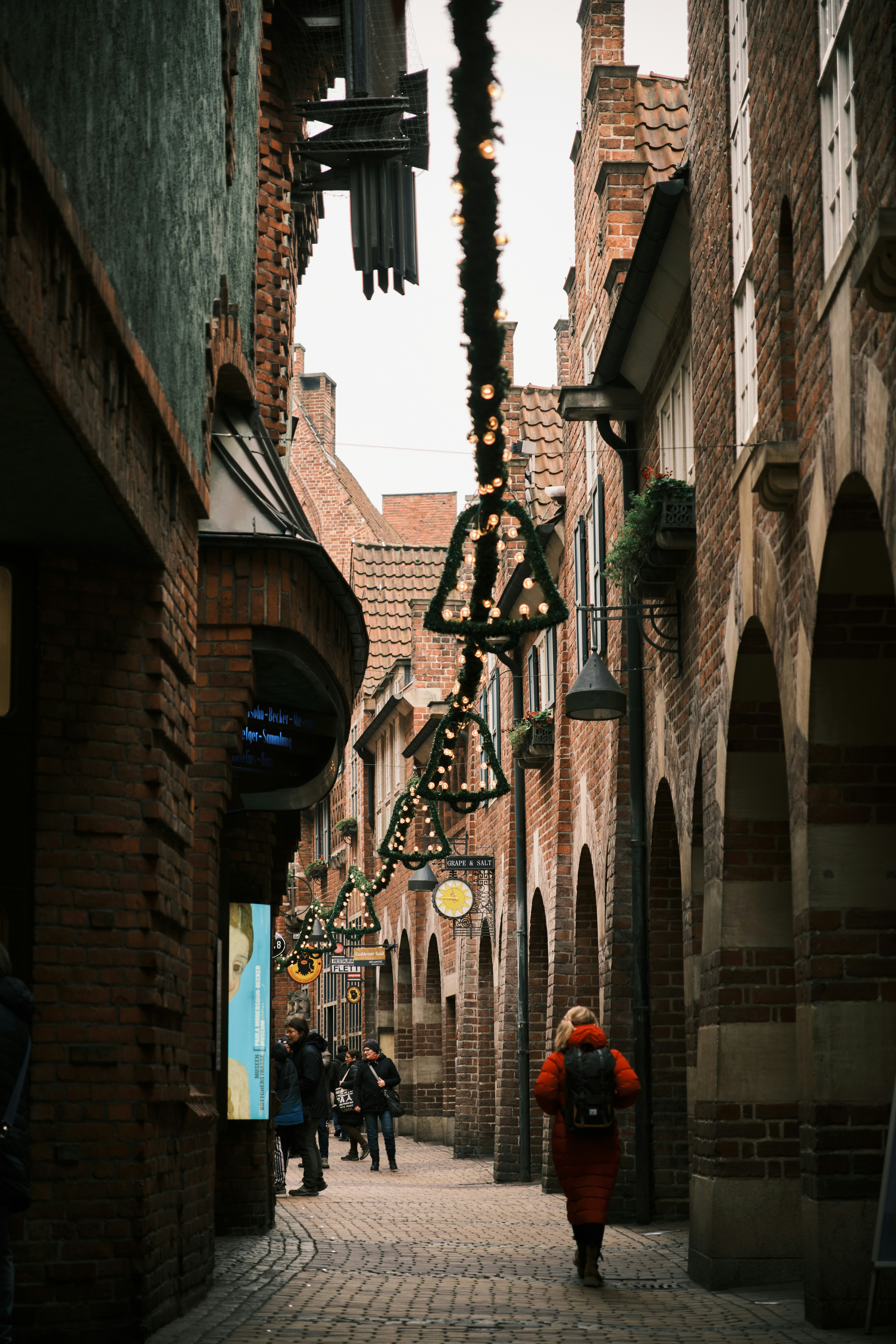 People walk down a cobblestone street decorated with bells.