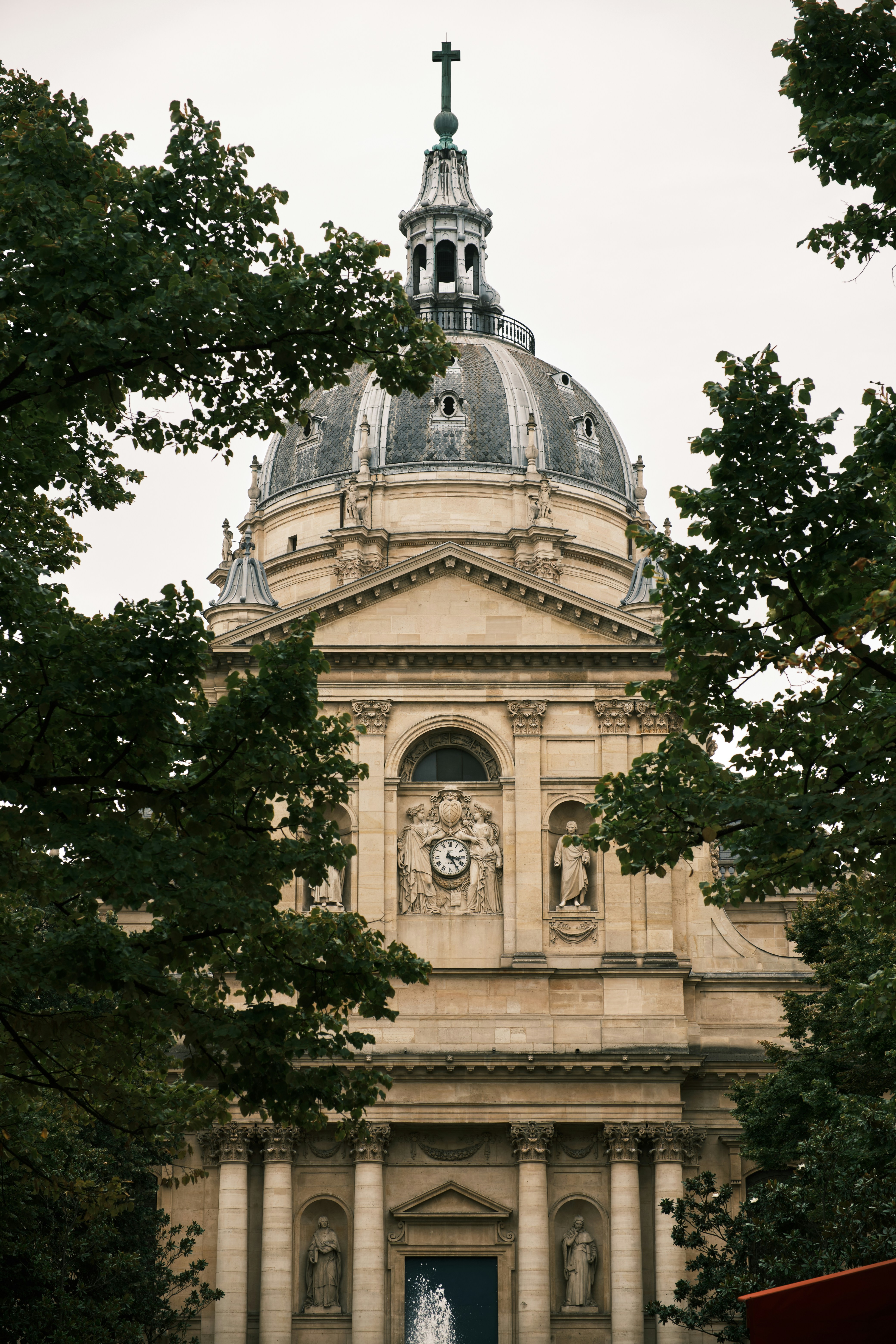 Historic dome structure framed by lush green foliage, showcasing intricate architectural details and a clock.
