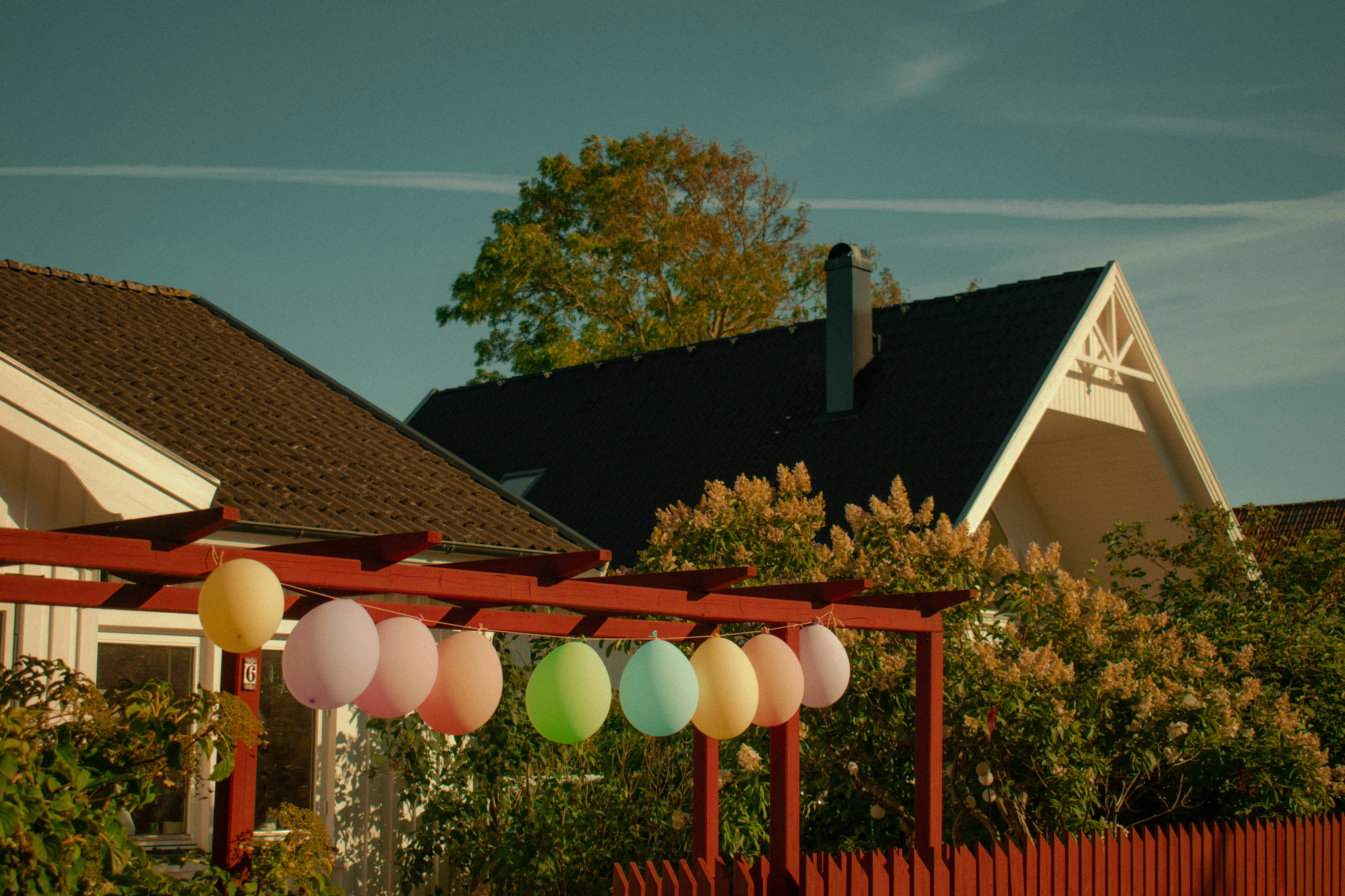 Colorful balloons hang from a wooden structure outside houses.