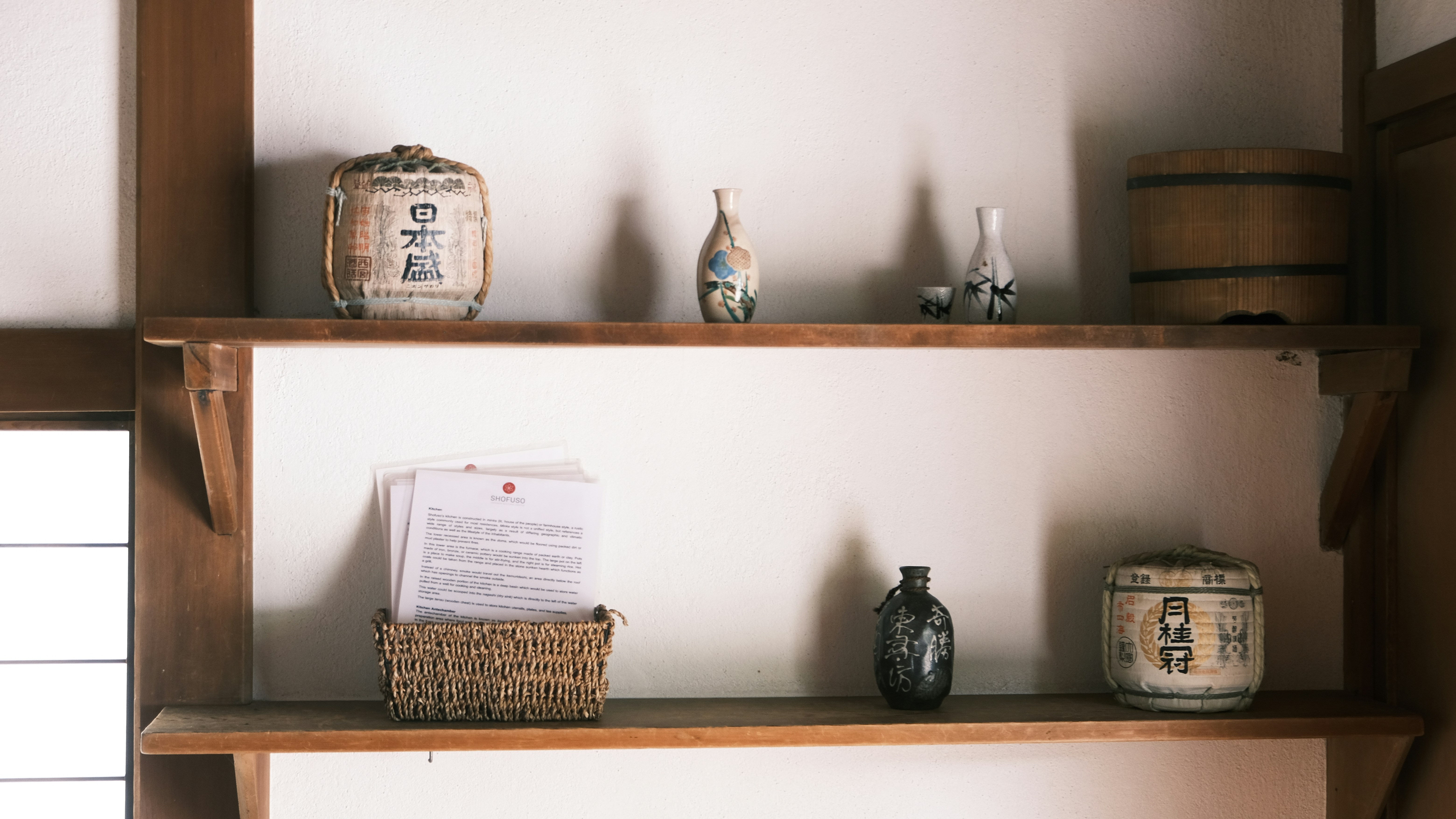 Wooden shelves display japanese sake barrels and bottles.