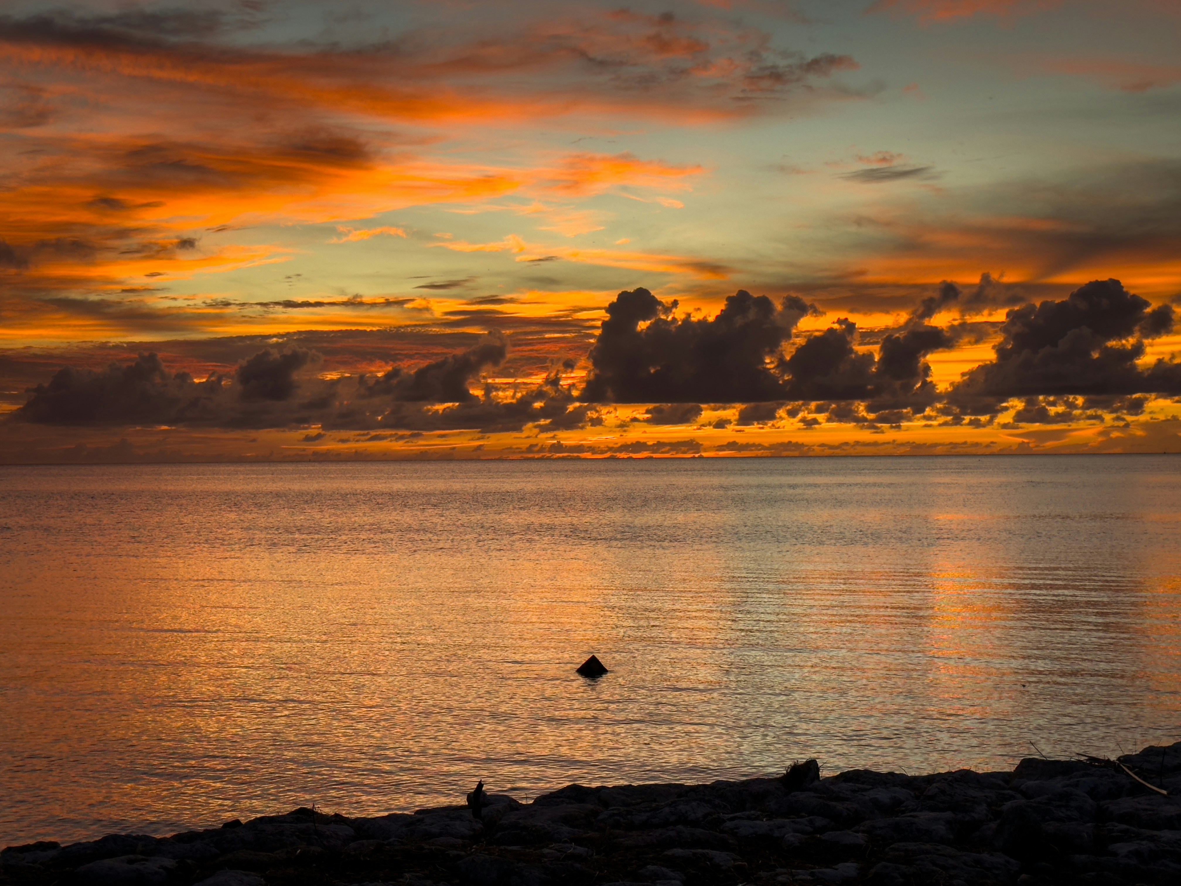 Sunset on Beach Road | Vibrant sunset over a calm ocean with rocky shore.