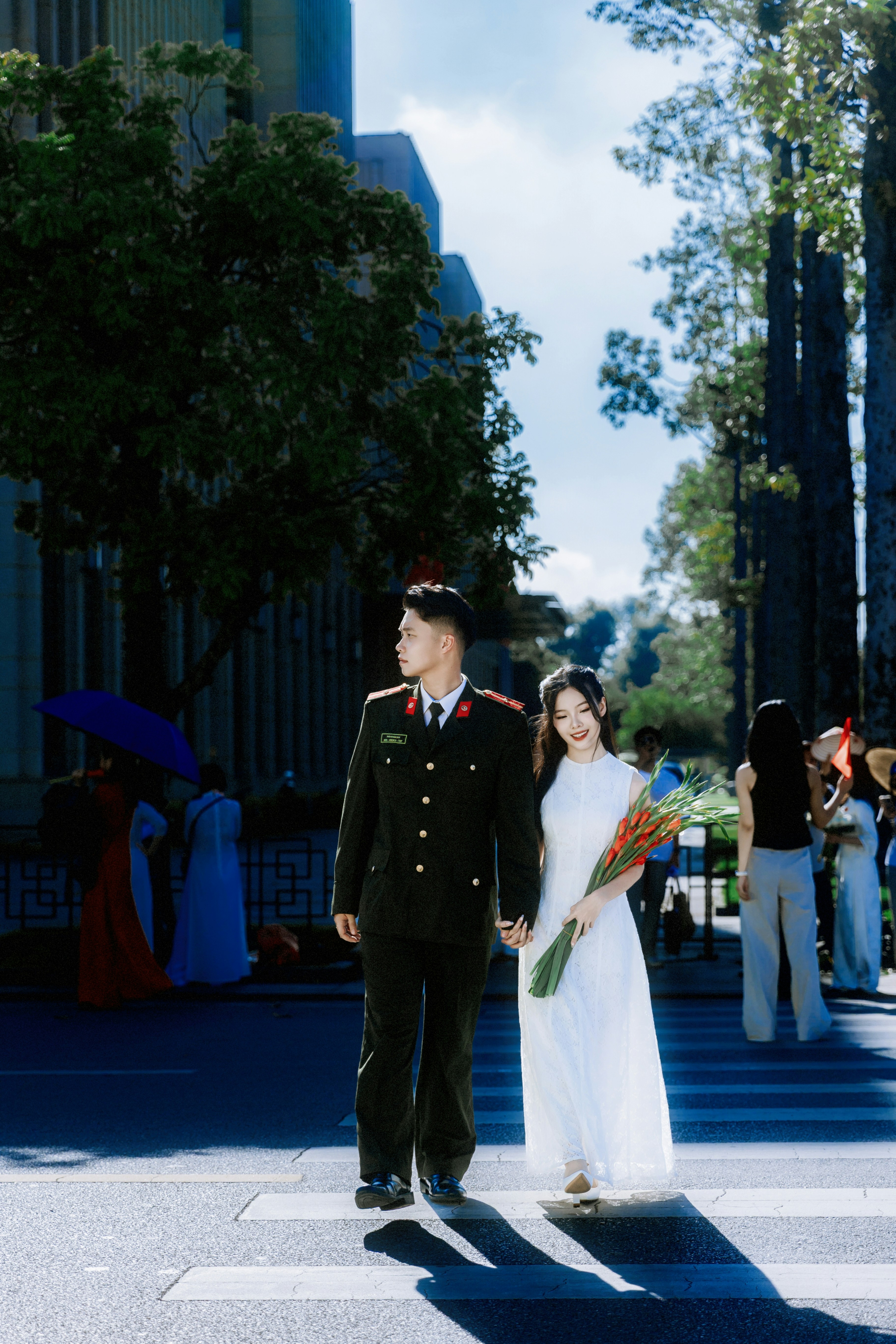 Couple portrait outdoors in Hanoi | Couple in uniform and white dress holding flowers on street