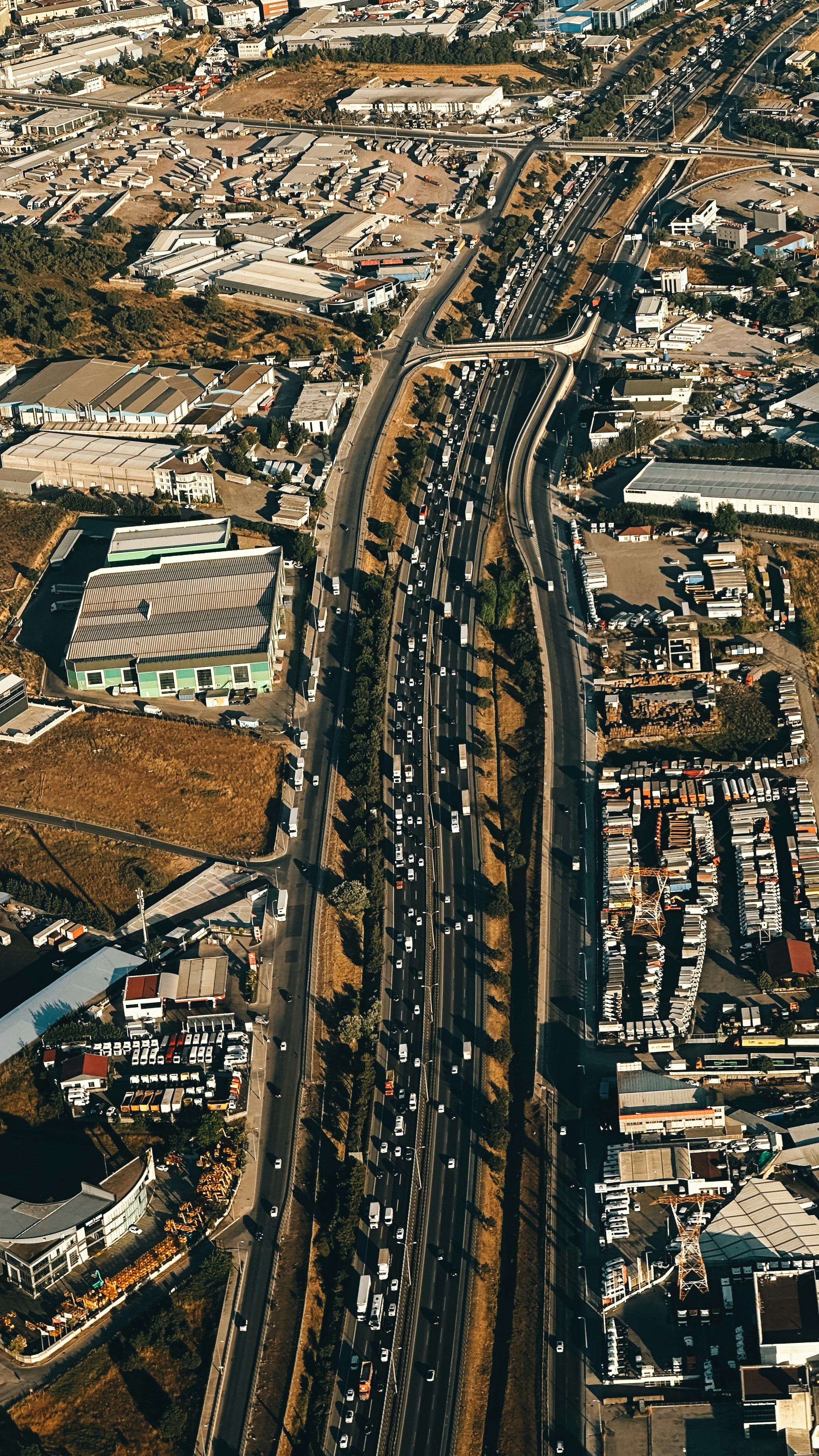 Aerial view of a busy highway surrounded by industrial buildings and organized chaos of vehicles. The scene captures the dynamic movement of urban transportation.
