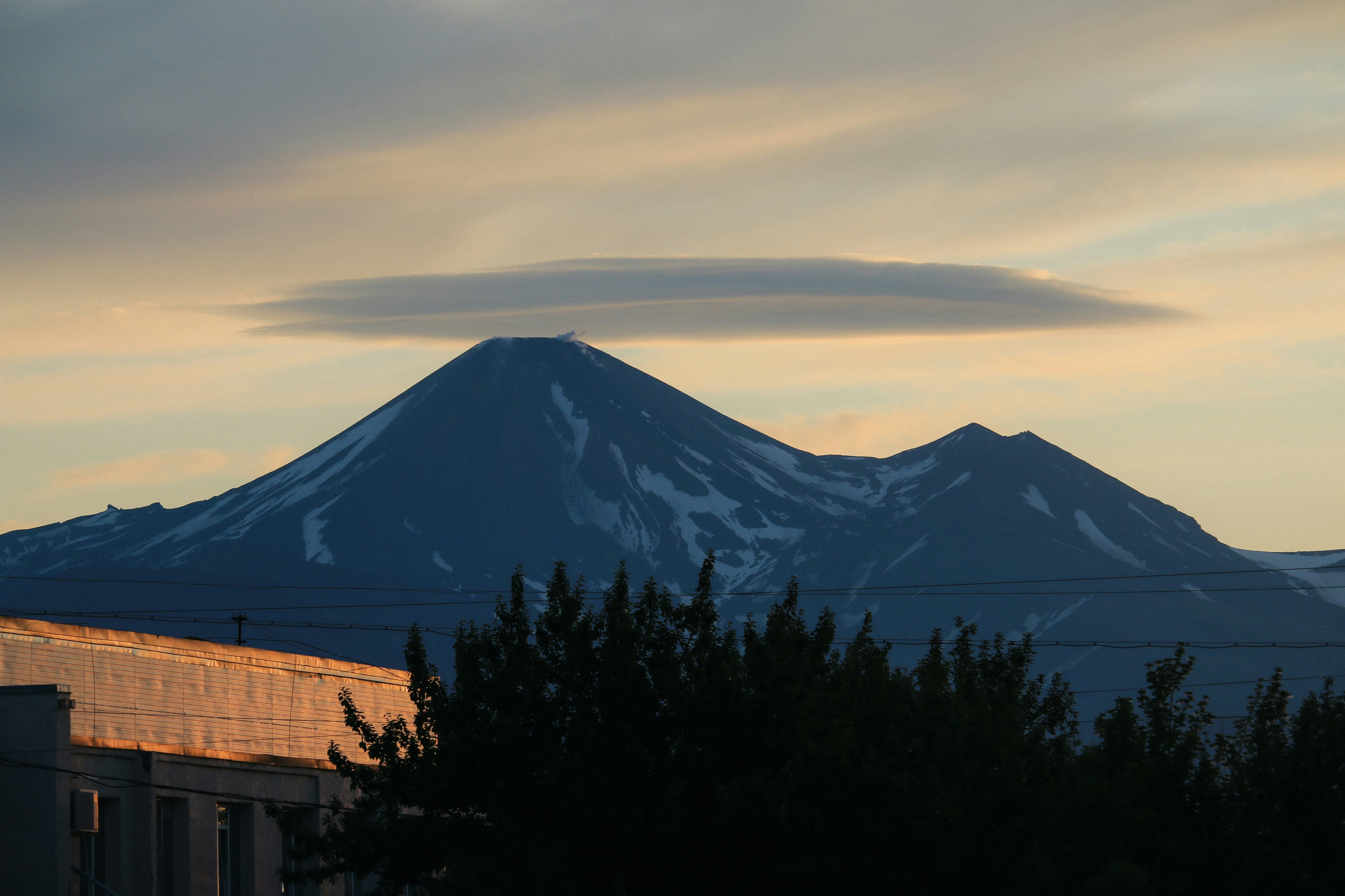 Snow-capped volcano under a lenticular cloud at sunset