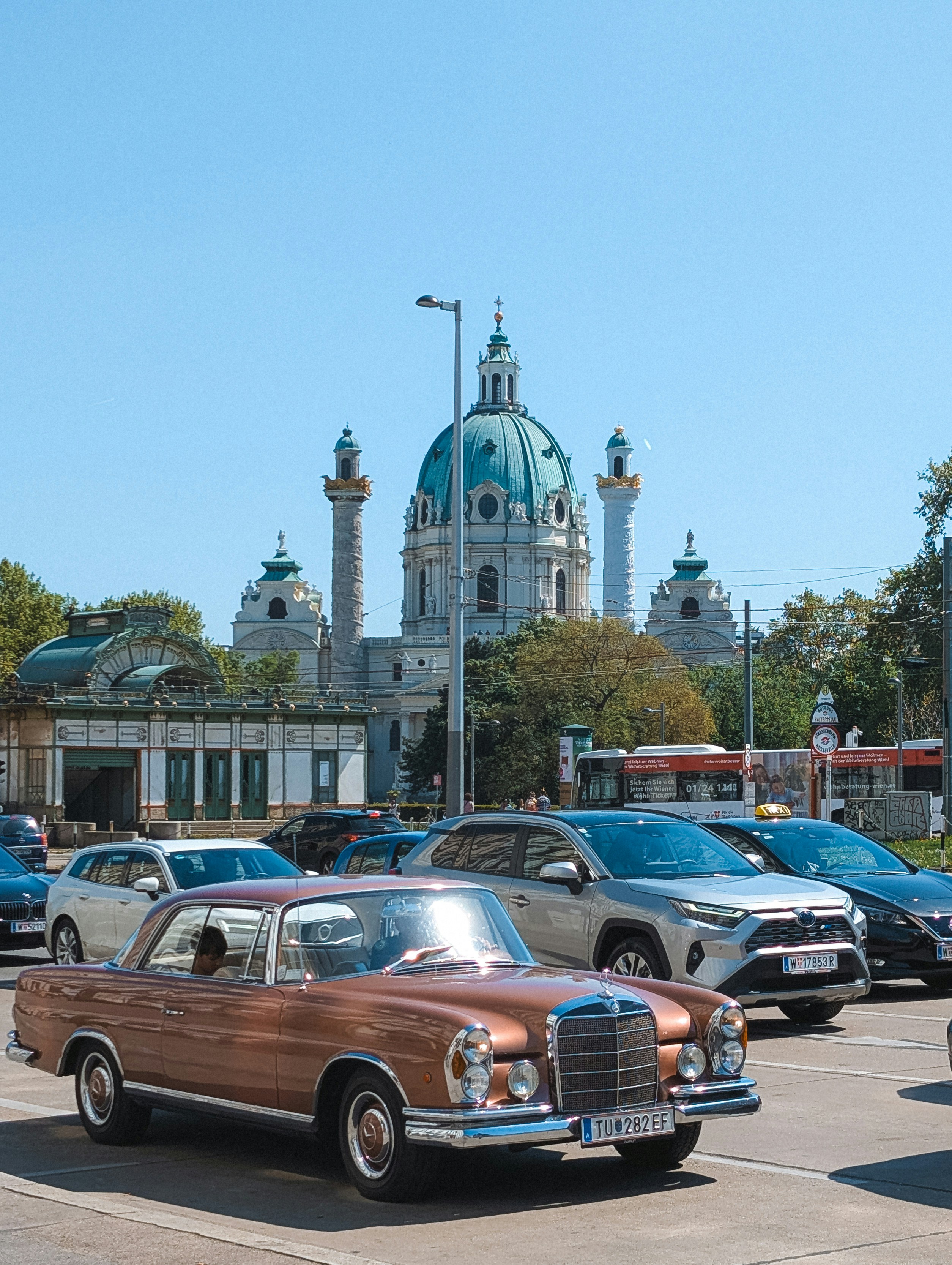 Classic Mercedes in traffic with church dome | Classic car drives past a grand building.