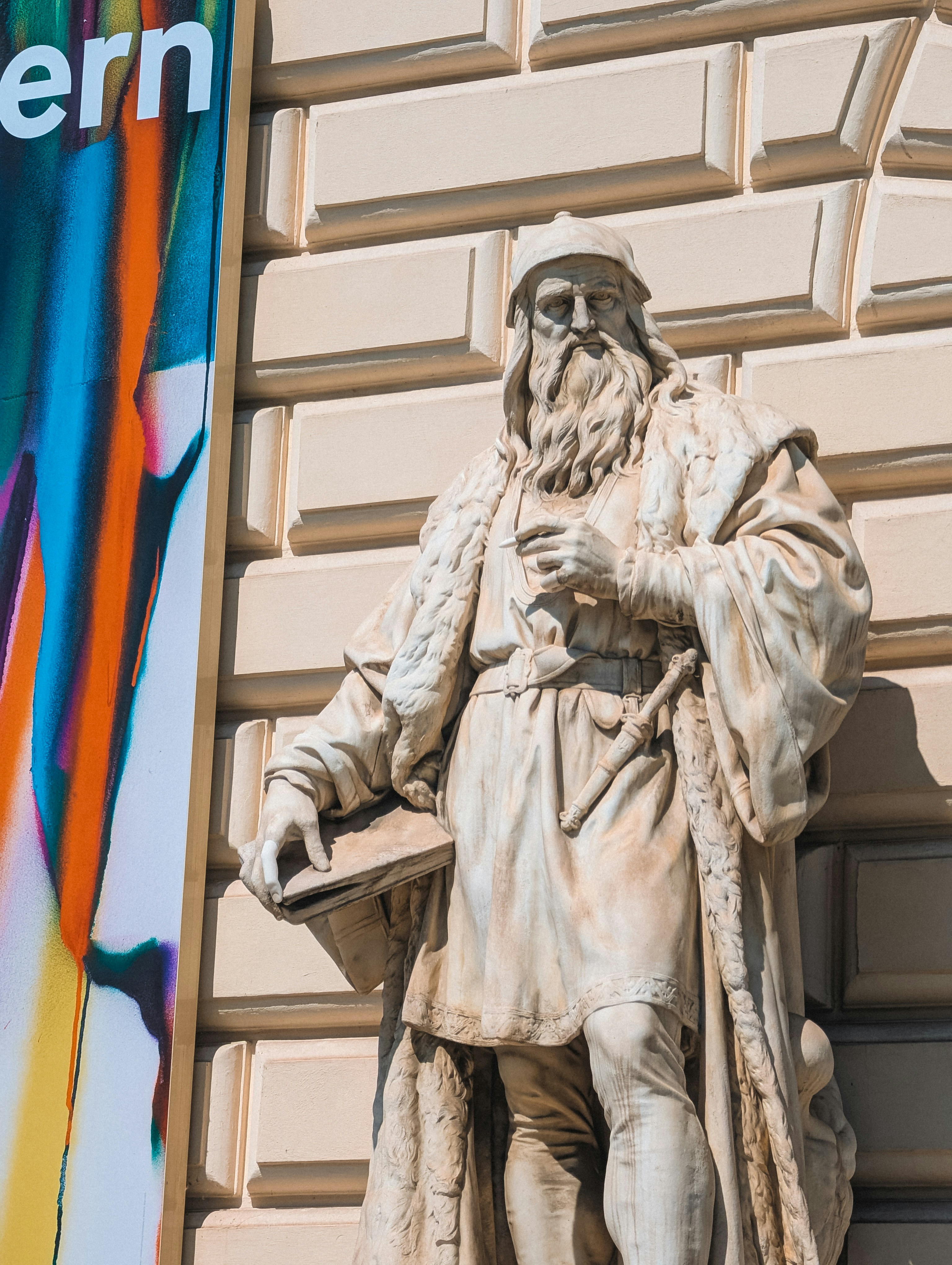 Stone statue outside a museum | Marble statue of man in historic clothing holding book.