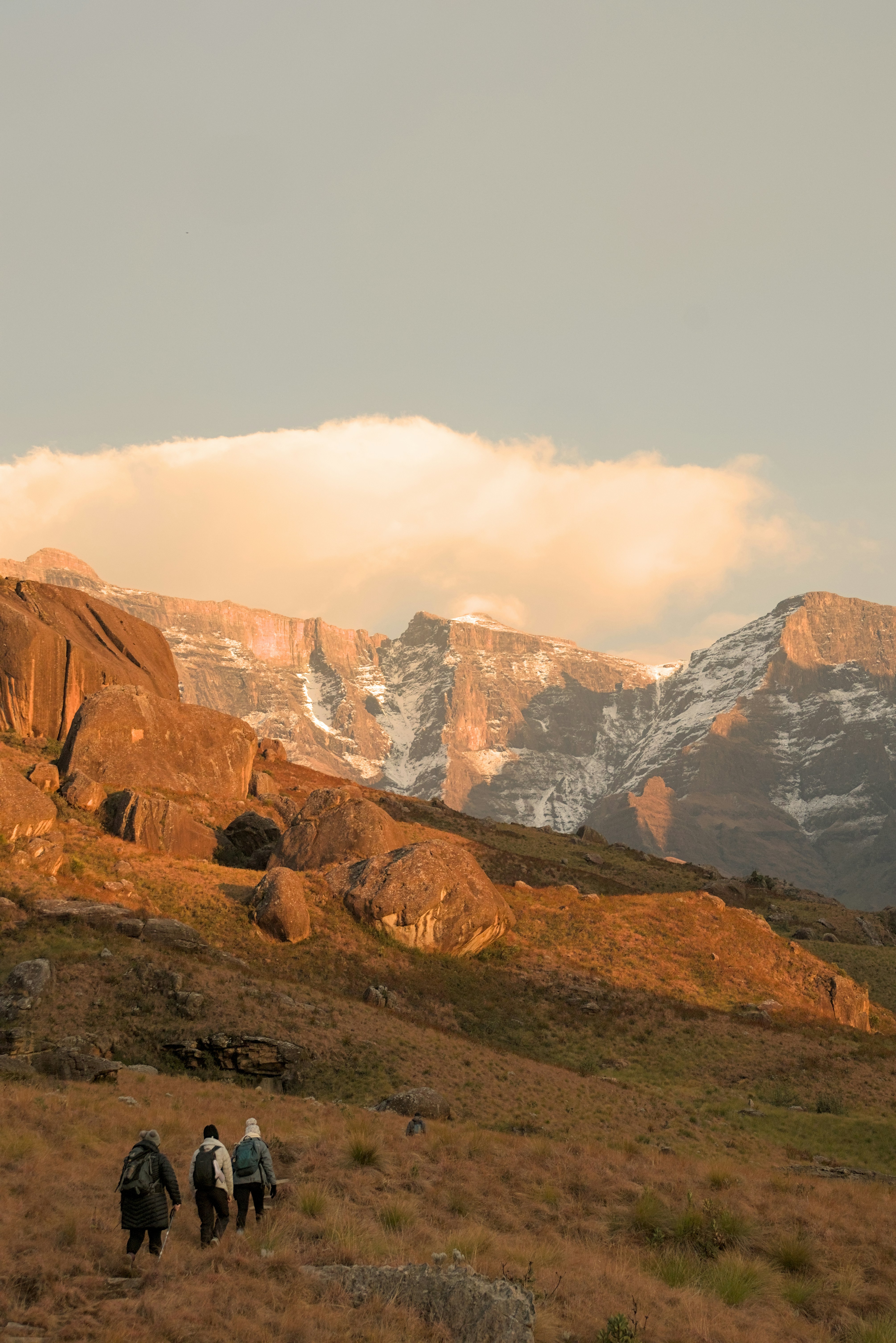 Drakensberg hike | Hikers ascend a grassy slope towards rocky mountains.