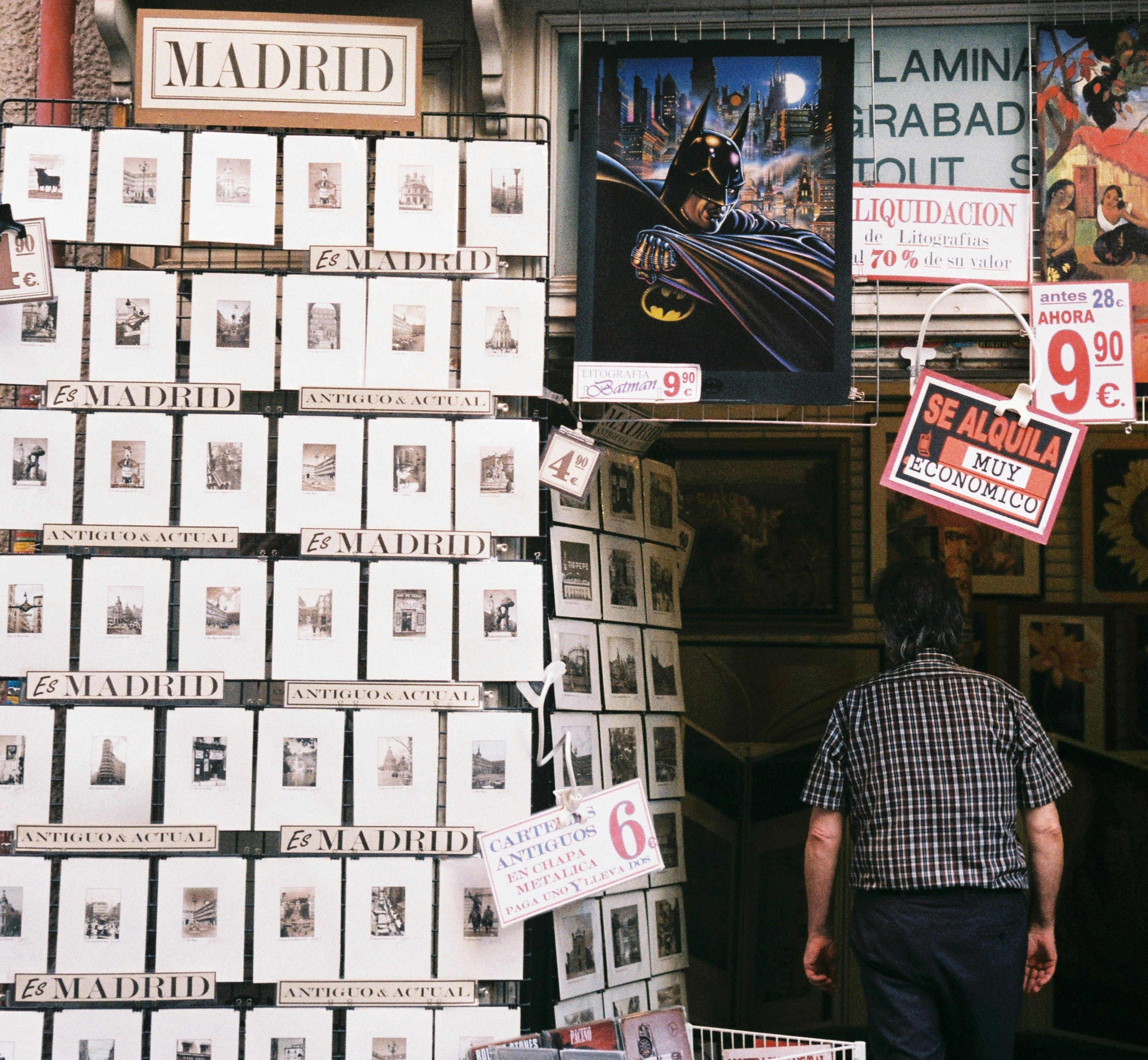 art shop owner | Man walks past a wall of small framed prints in madrid.