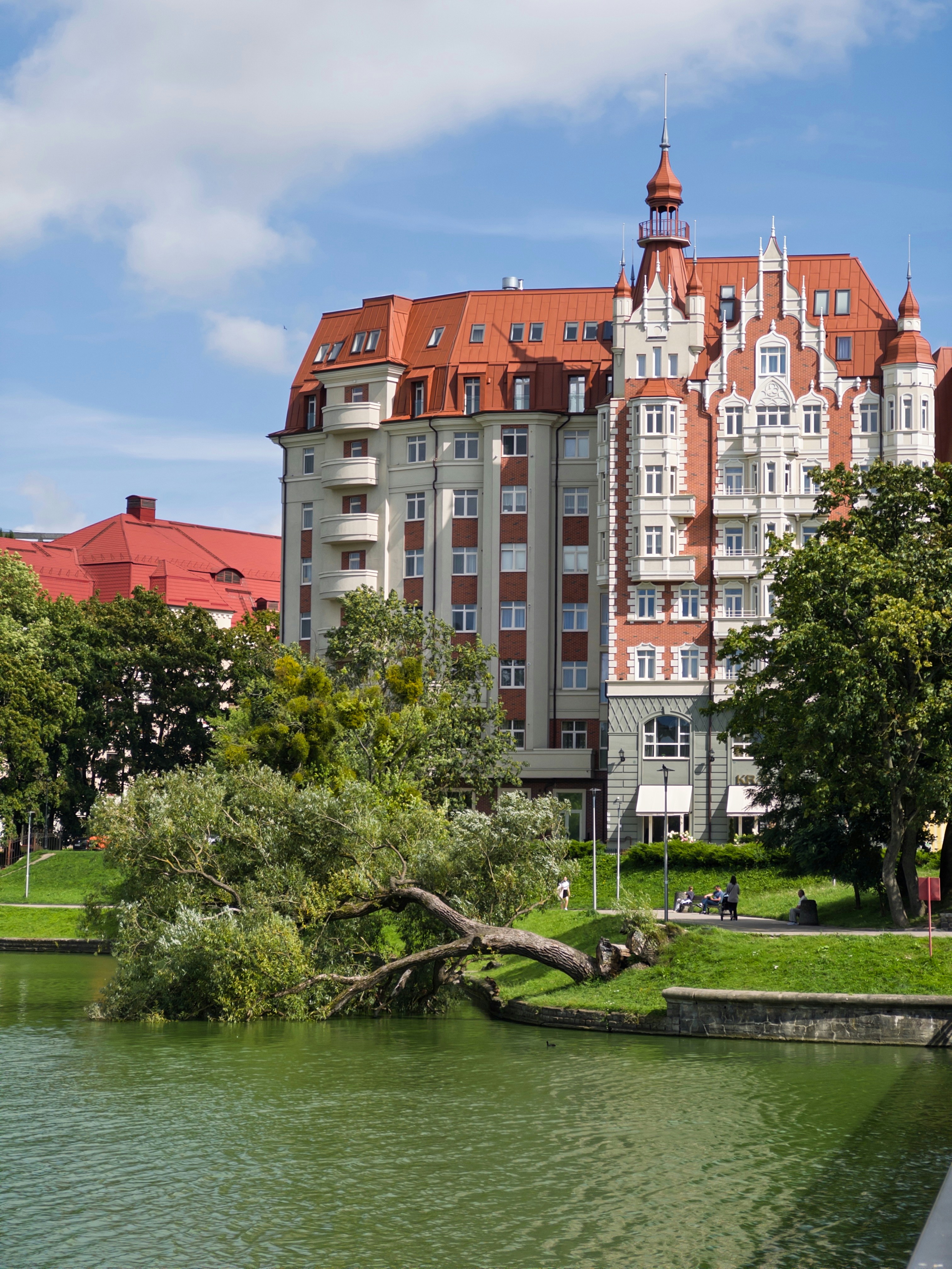 Ornate building with red roof beside a green river.