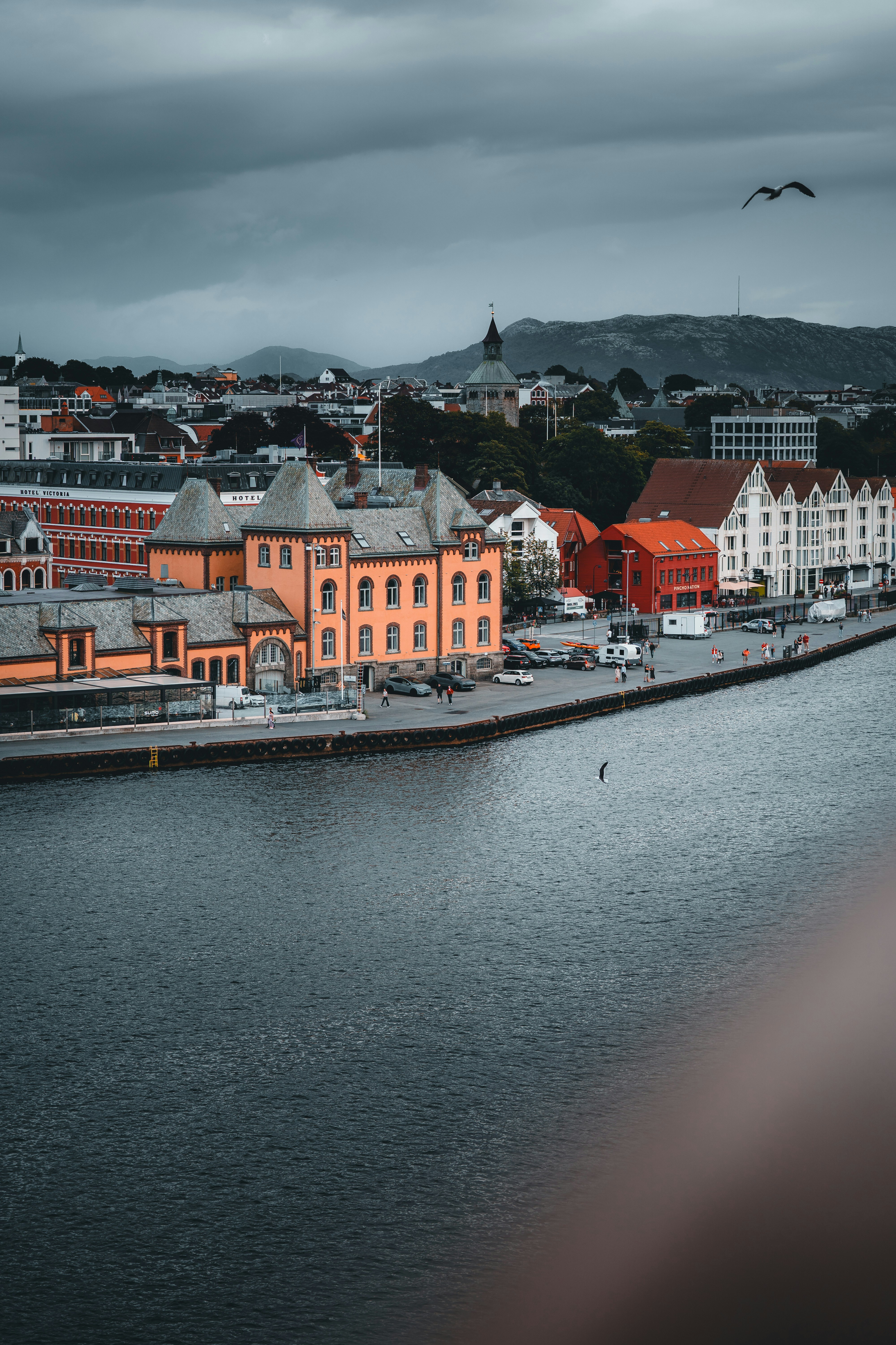 Vibrant orange building alongside a tranquil harbor, surrounded by a mix of modern and historic architecture under a cloudy sky.