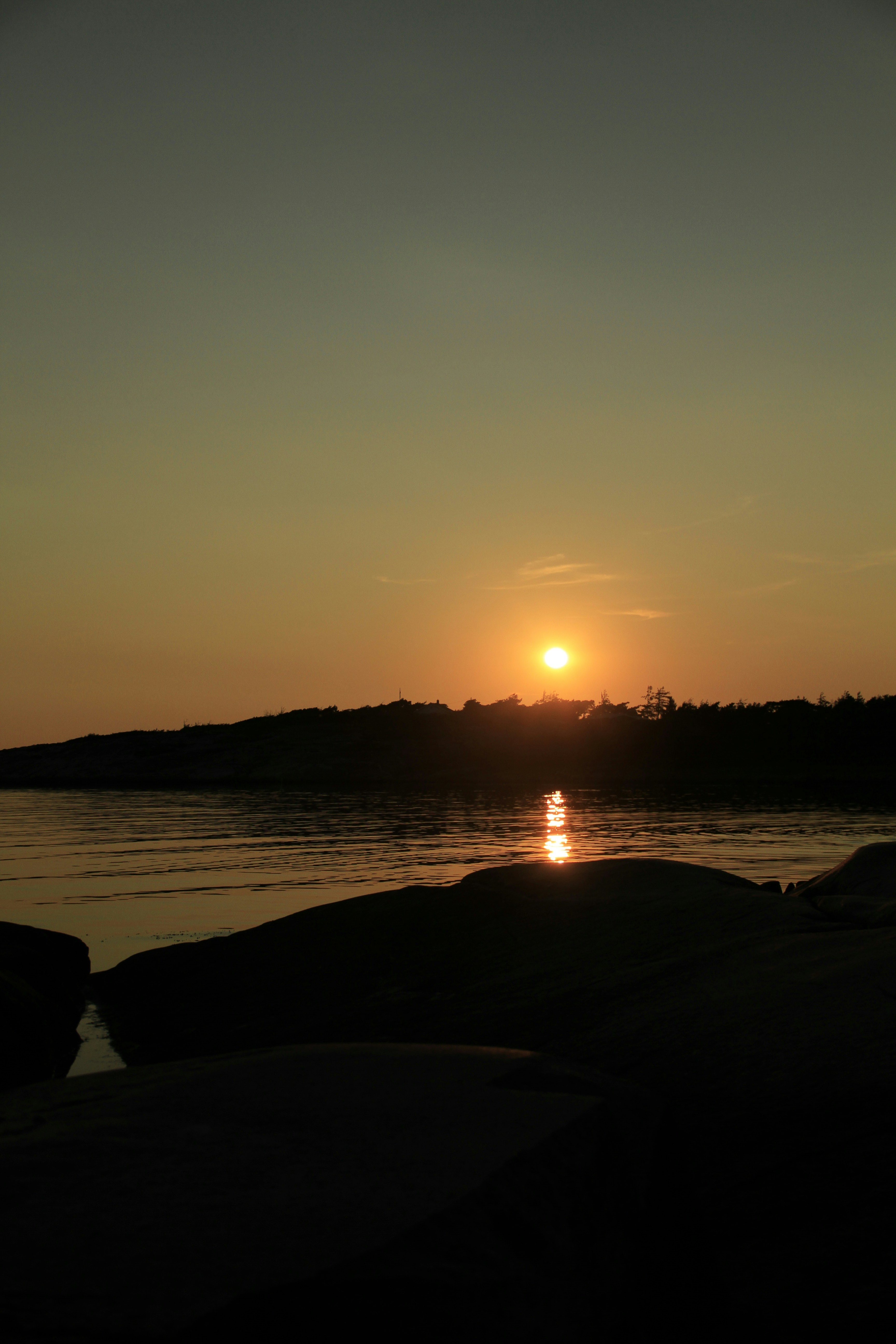 Golden sunset casting reflections on calm waters, framed by silhouettes of distant trees and rocks.