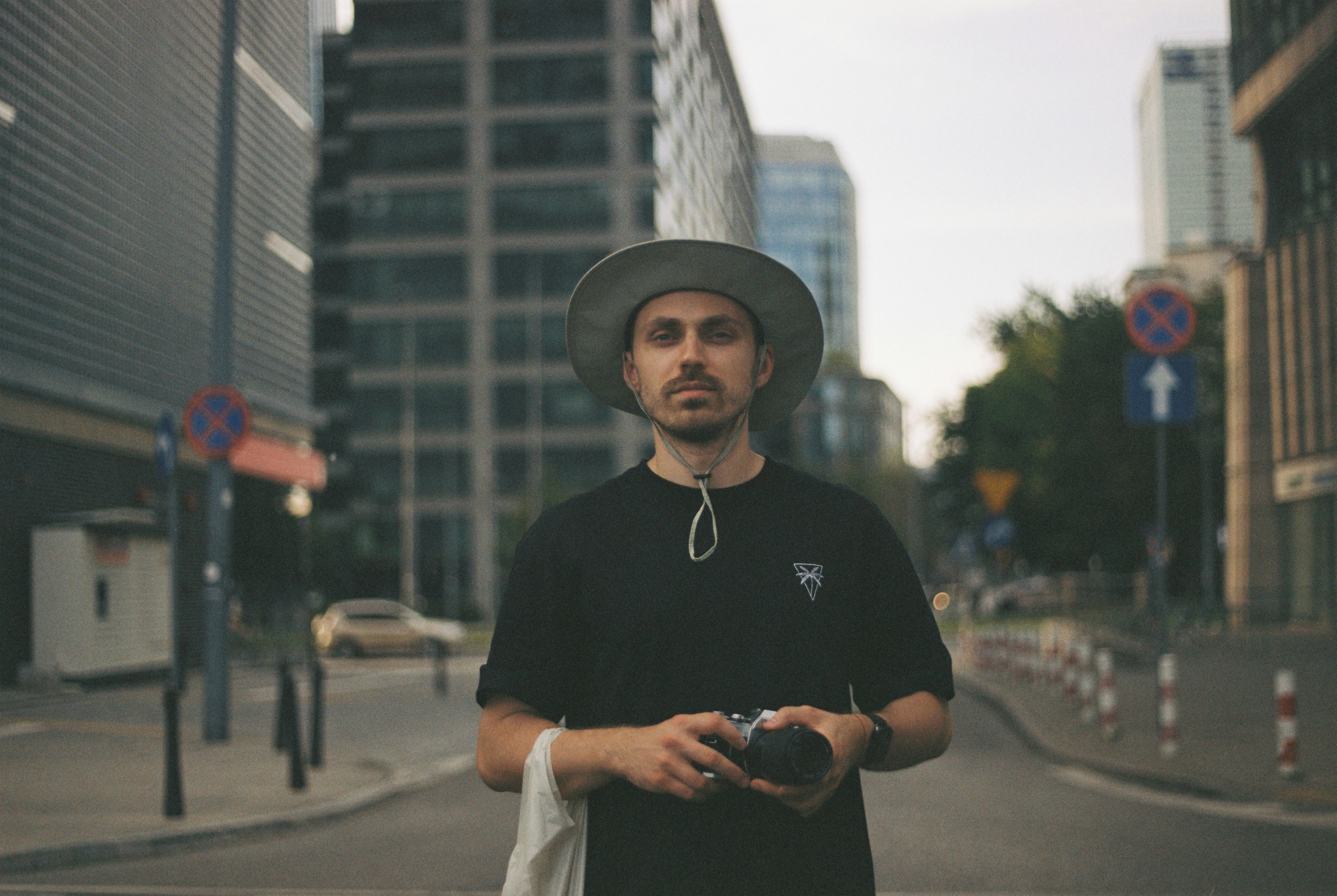 Man in hat holding camera on city street