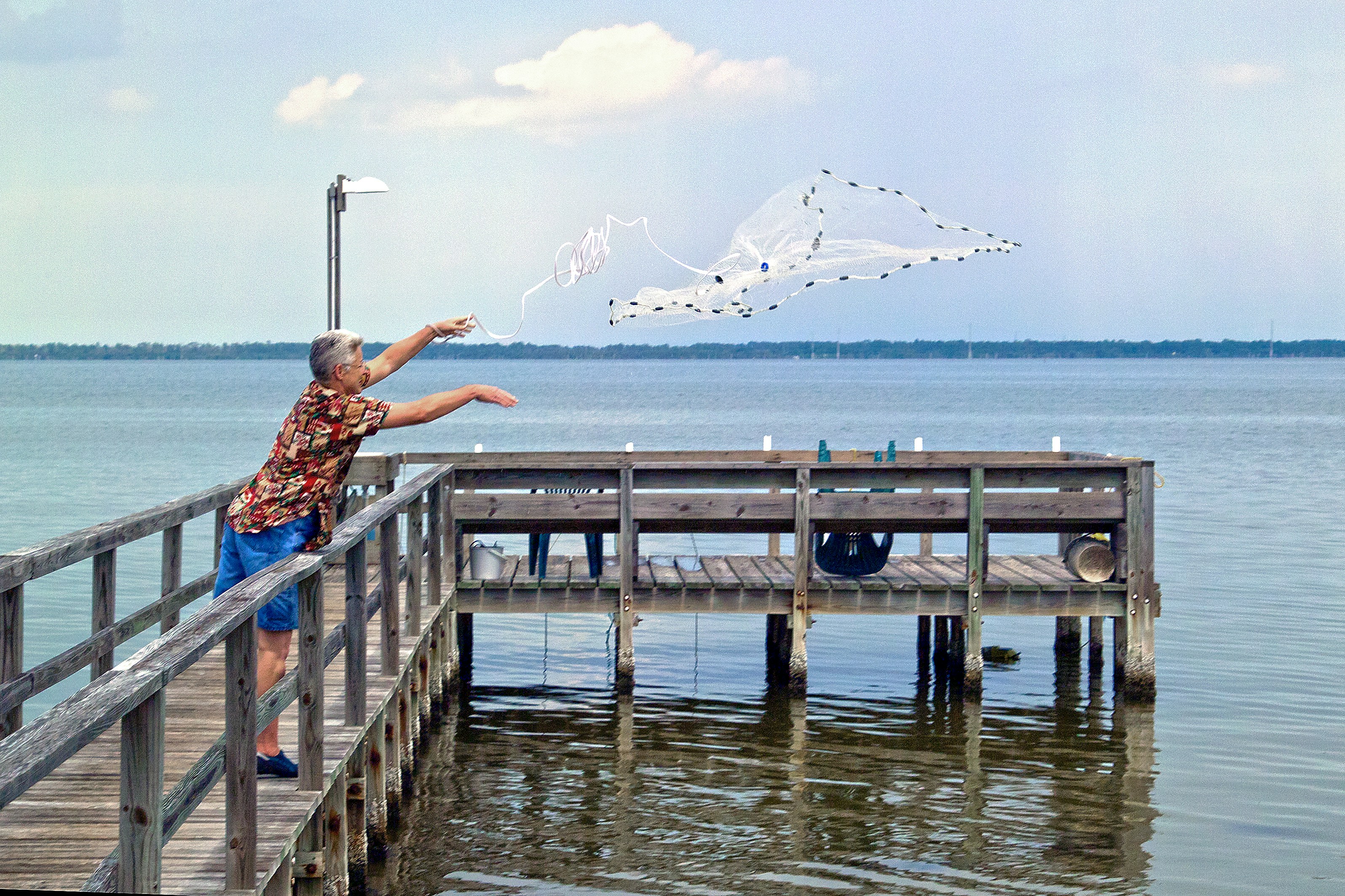 The art of casting a bait net. | Man casting a fishing net from a pier.