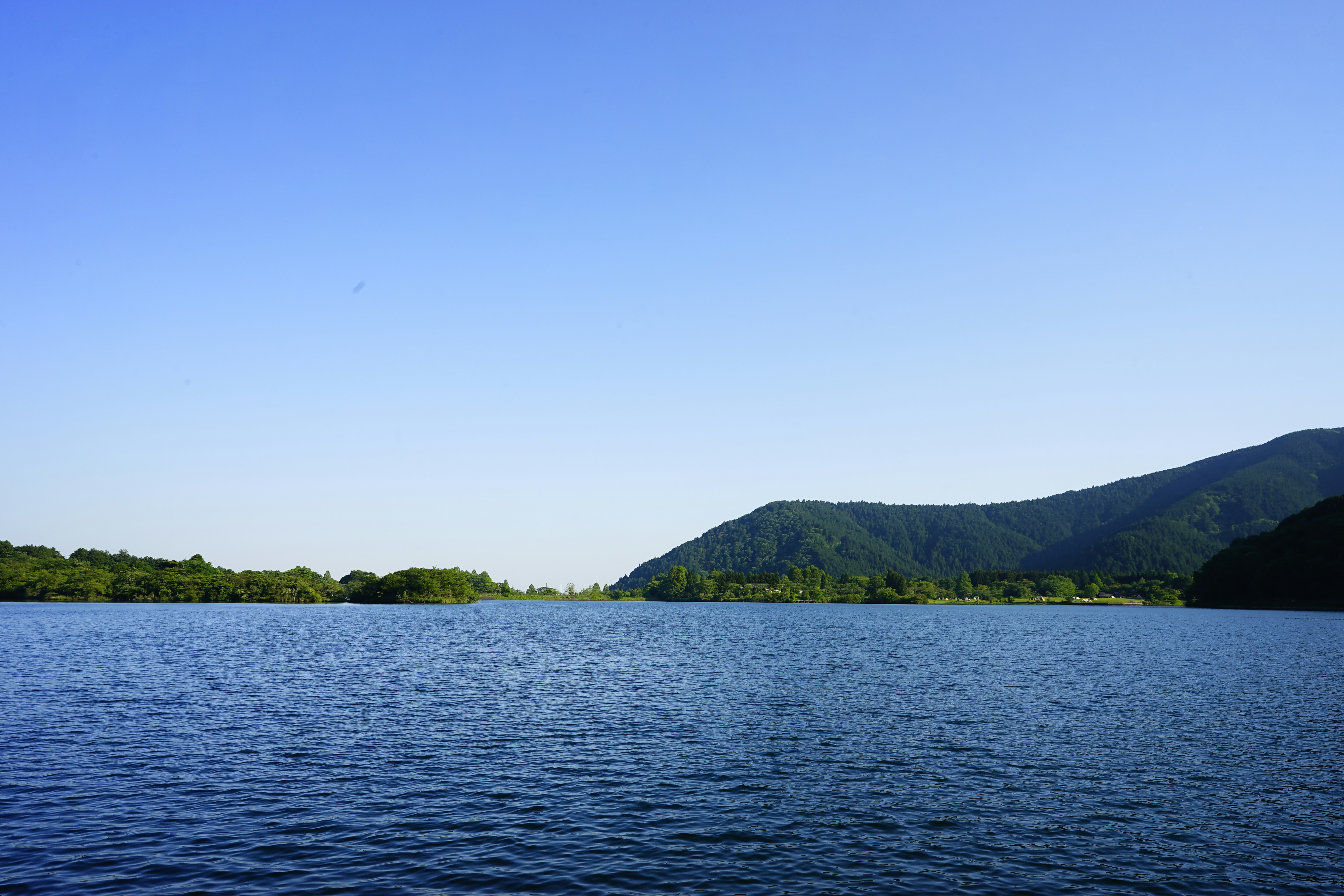 Calm blue lake with green hills under clear sky