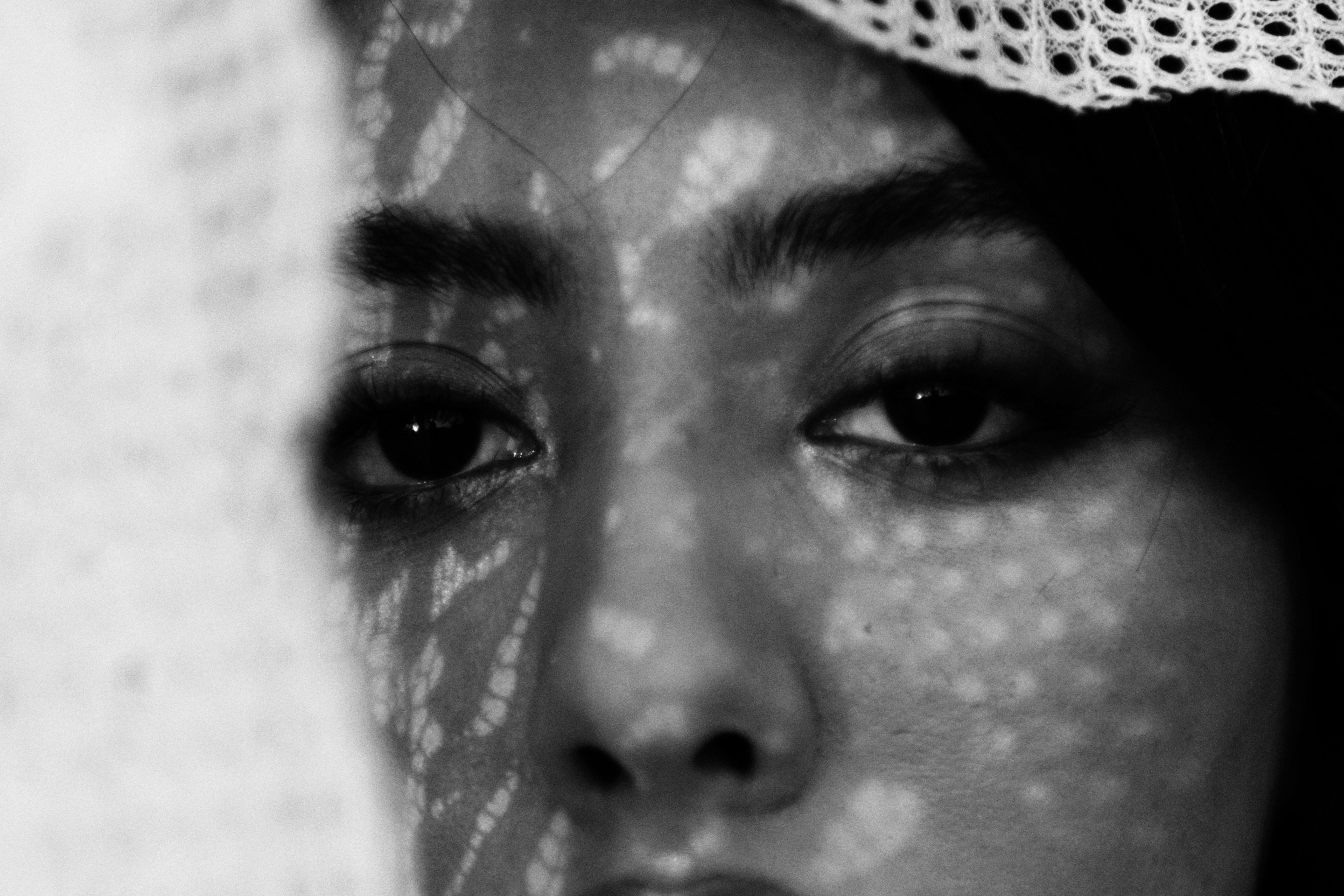 Close-up portrait featuring a woman's face partially obscured by a delicate lace pattern casting intricate shadows.